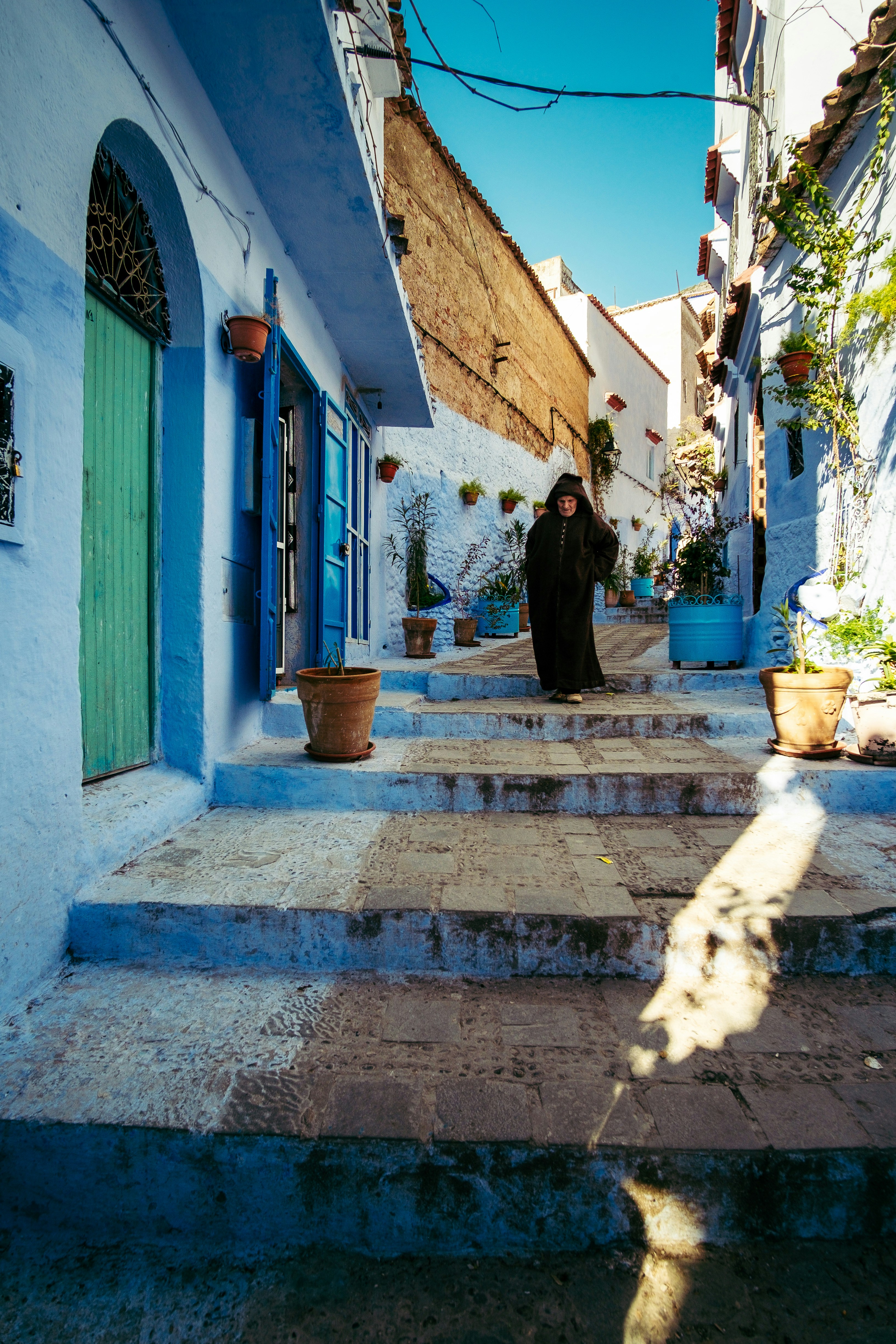 Azure Alleyway Portrait: A Cloaked Figure on Moroccan Blue Steps
