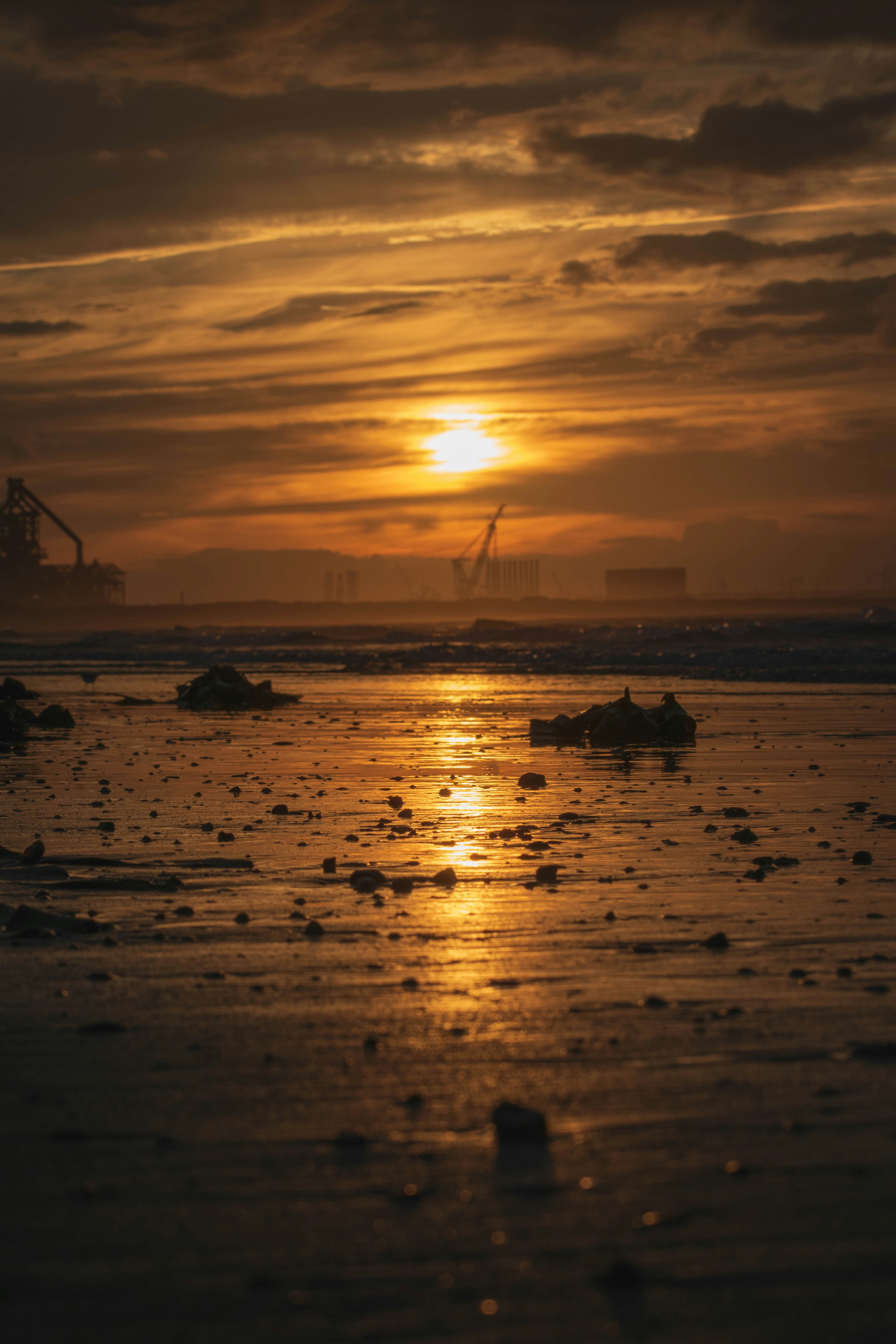 Crimson Dusk Over the Industrial Shoreline: Sun, Sand, and Silent Cranes