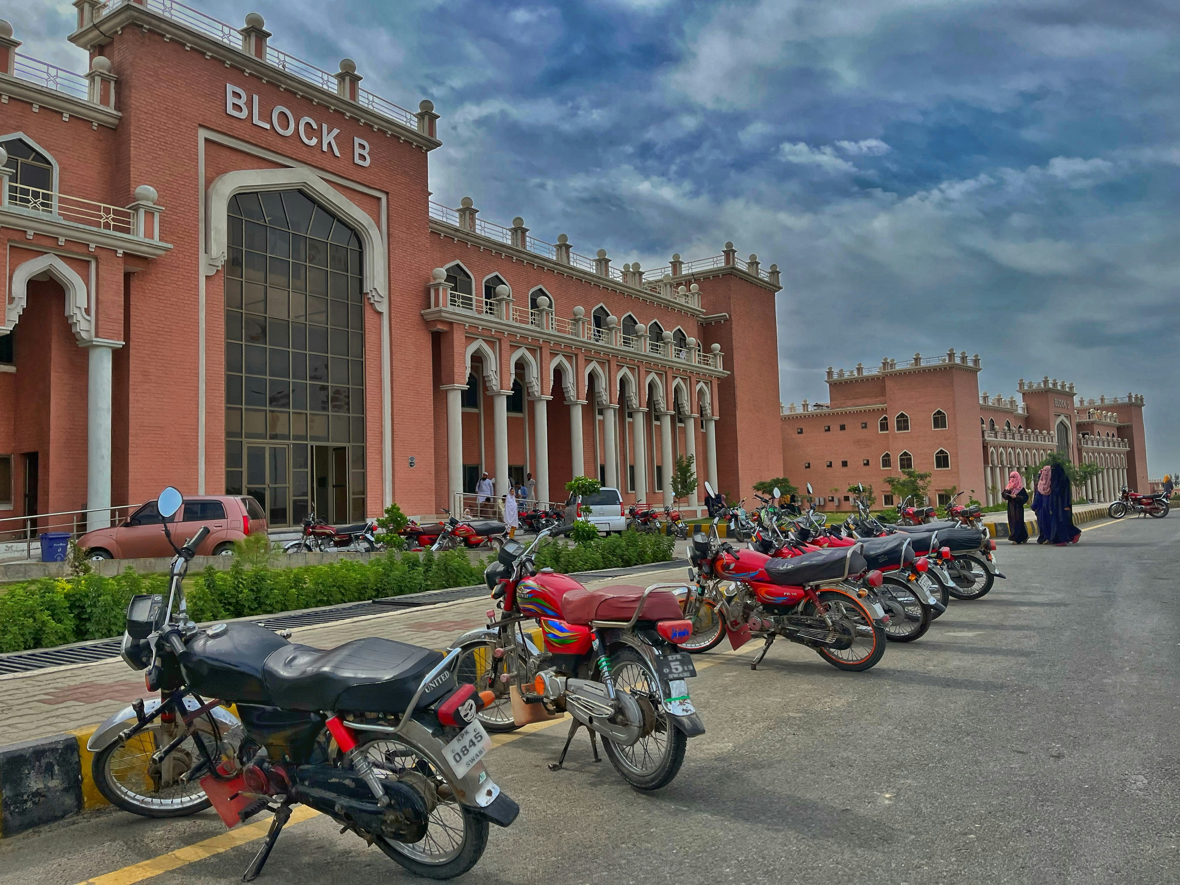 Bikes parked in front of a grand university brick building under a cloudy sky.