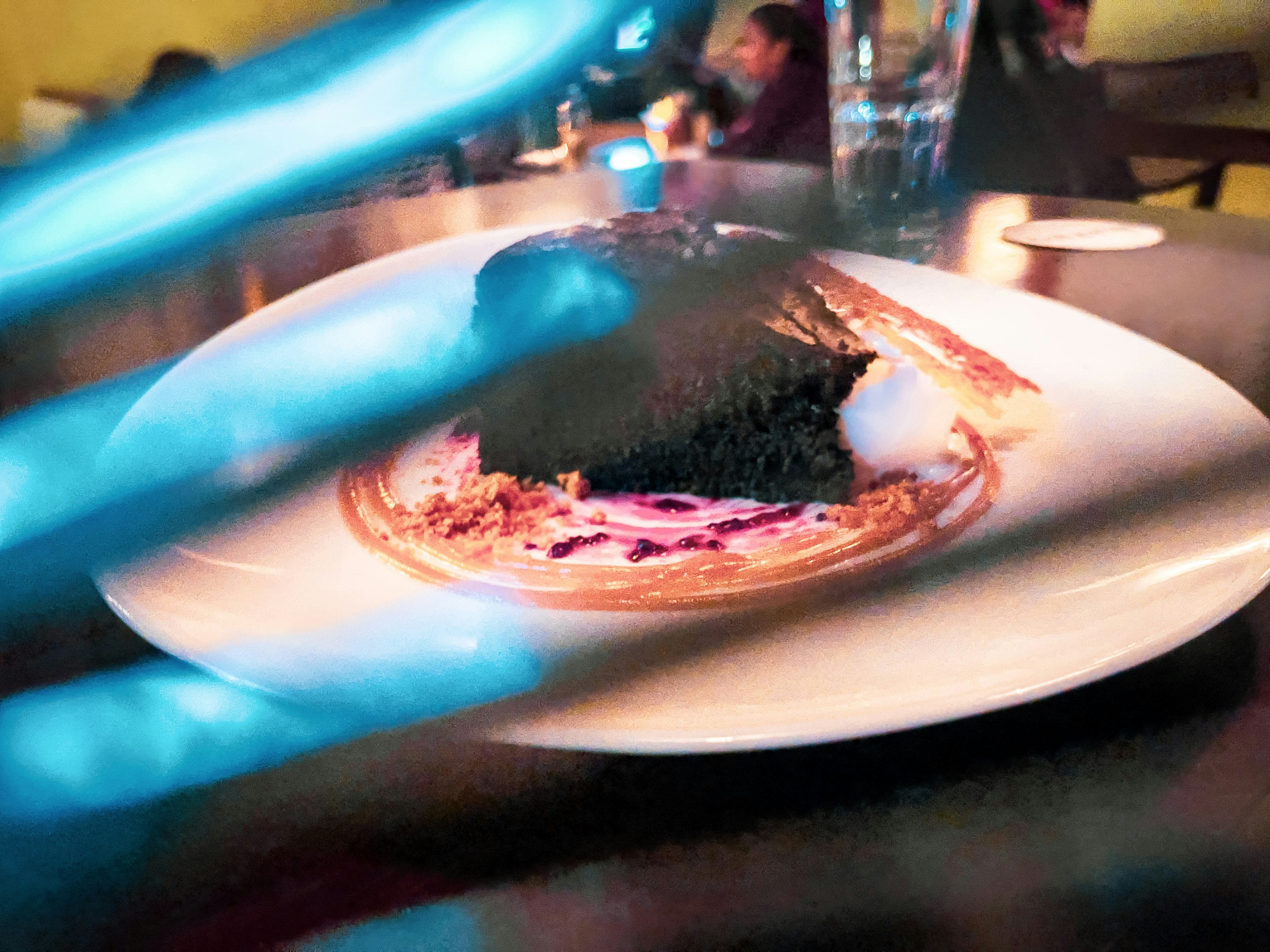 Dark Block Cake Anchored on a Syrup Ring Under Neon Blue Blur
