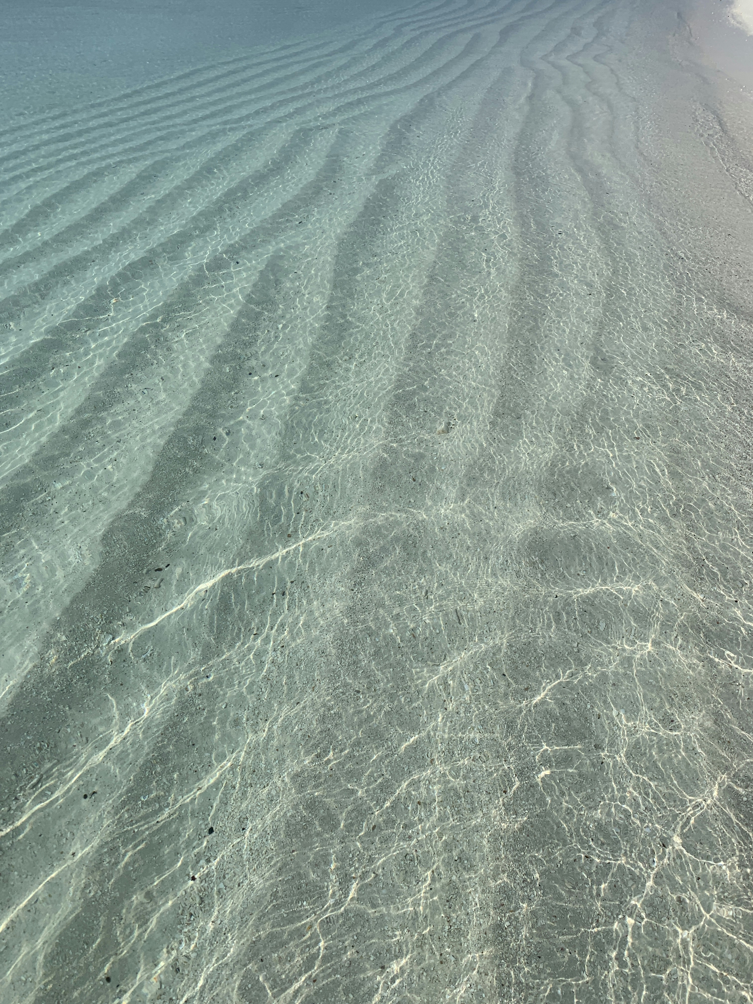 Gentle ripples create mesmerizing patterns on the clear water's surface, reflecting sunlight in a tranquil coastal scene.