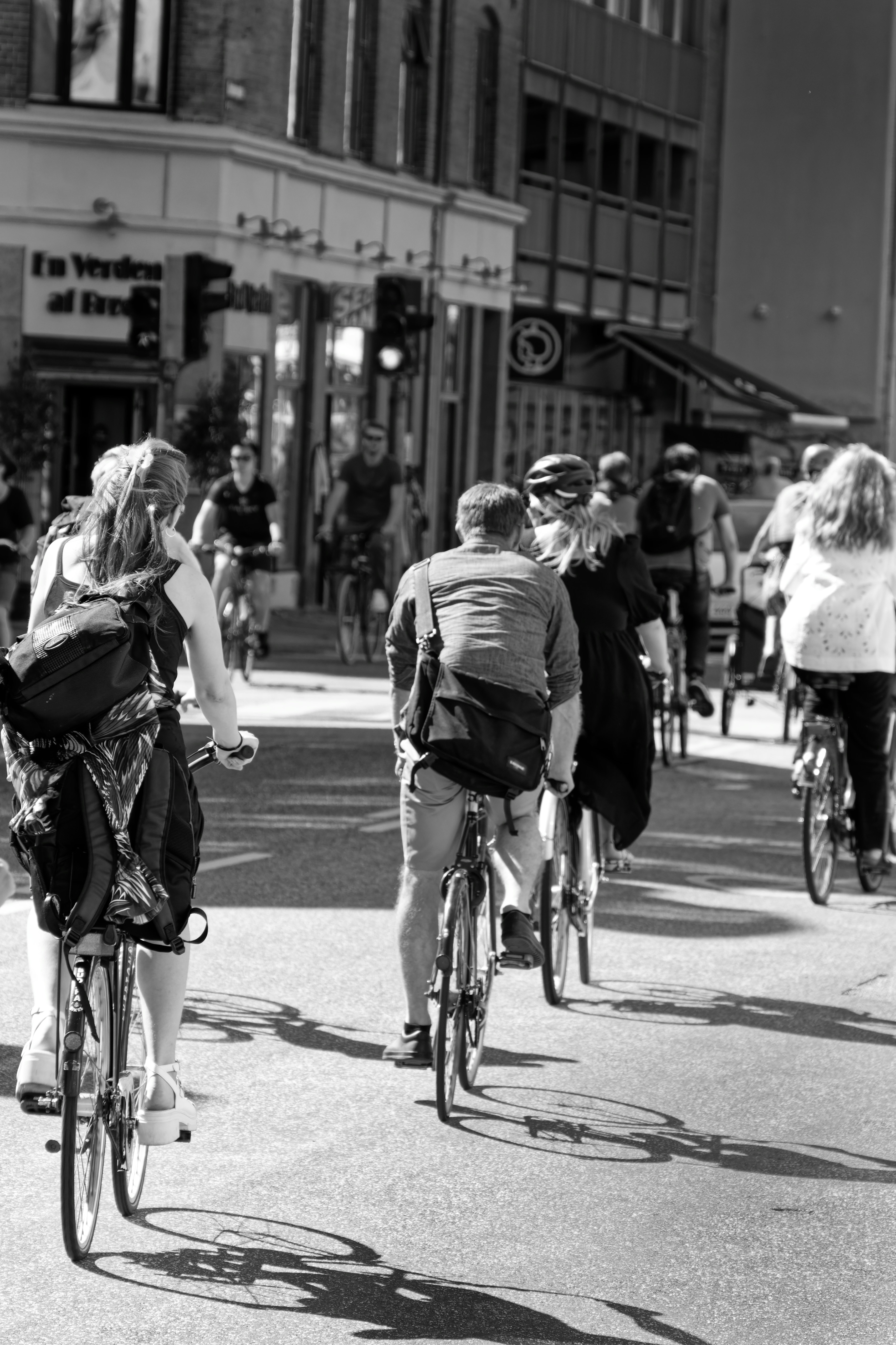 Group of cyclists rides through a busy city street, viewed from behind in a black-and-white photograph.