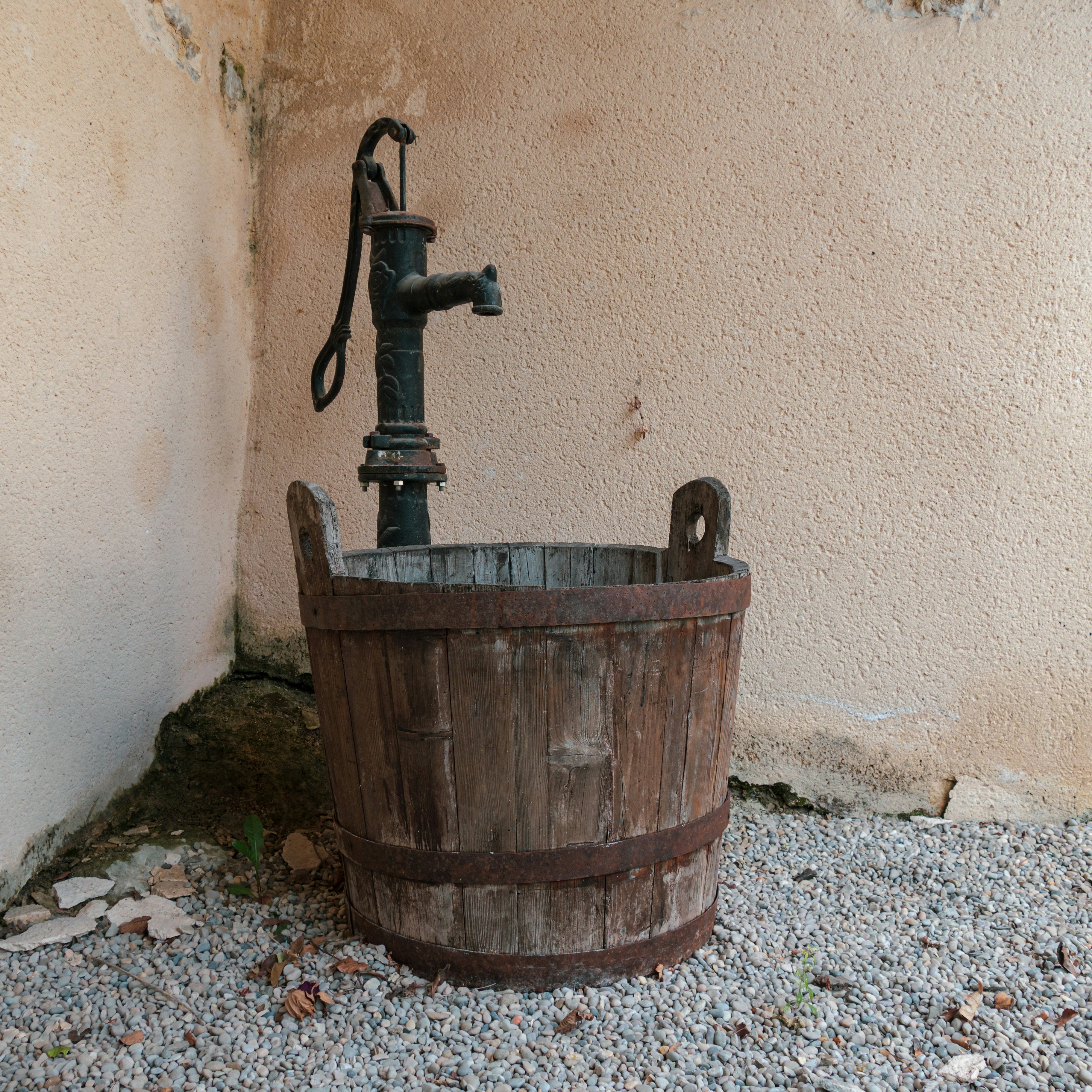 Rust and water: a vintage hand pump rising from a wooden tub in a sunlit courtyard