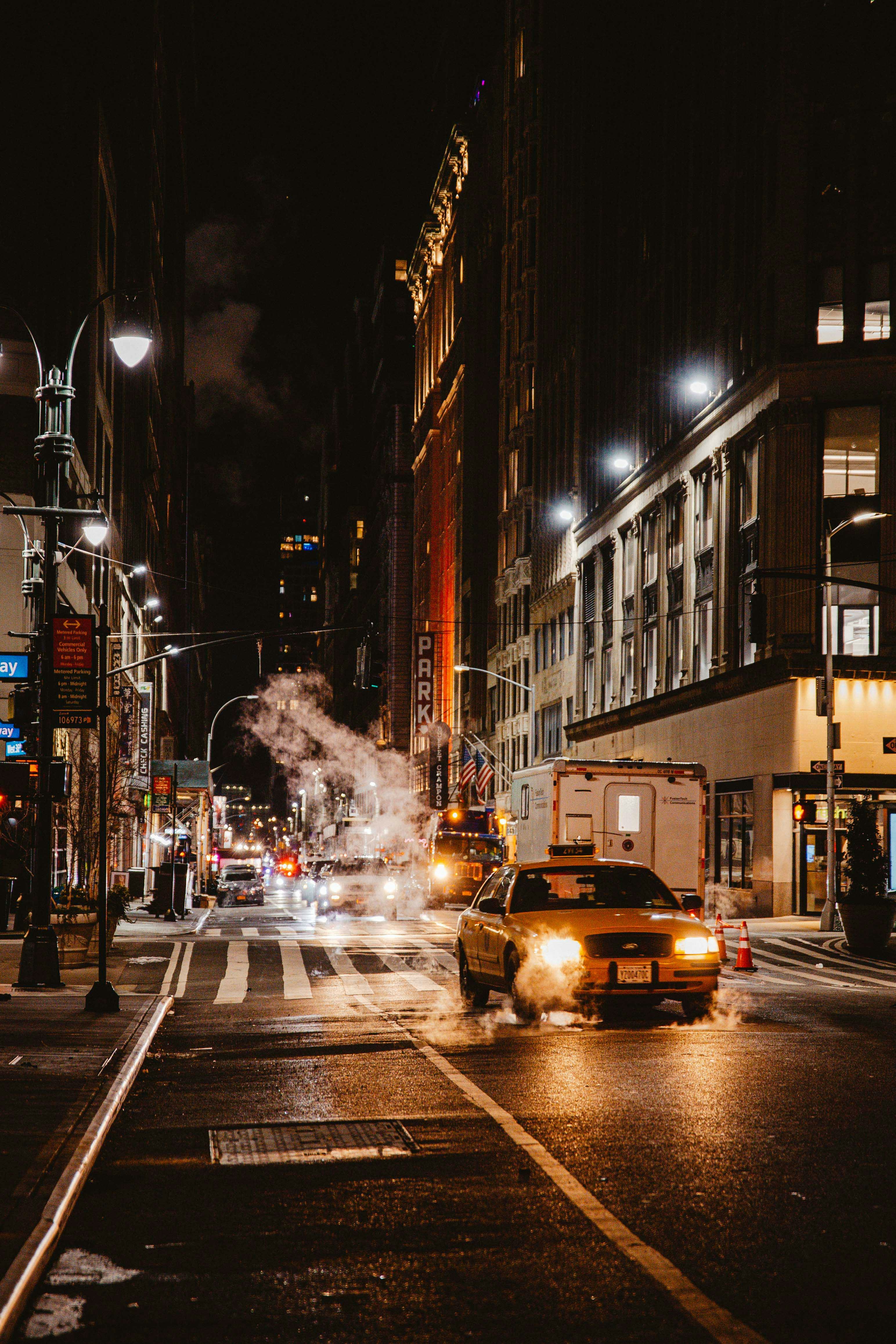 Yellow Taxi Breathing Steam Under Neon Night on a Rain-Warmed Downtown Street