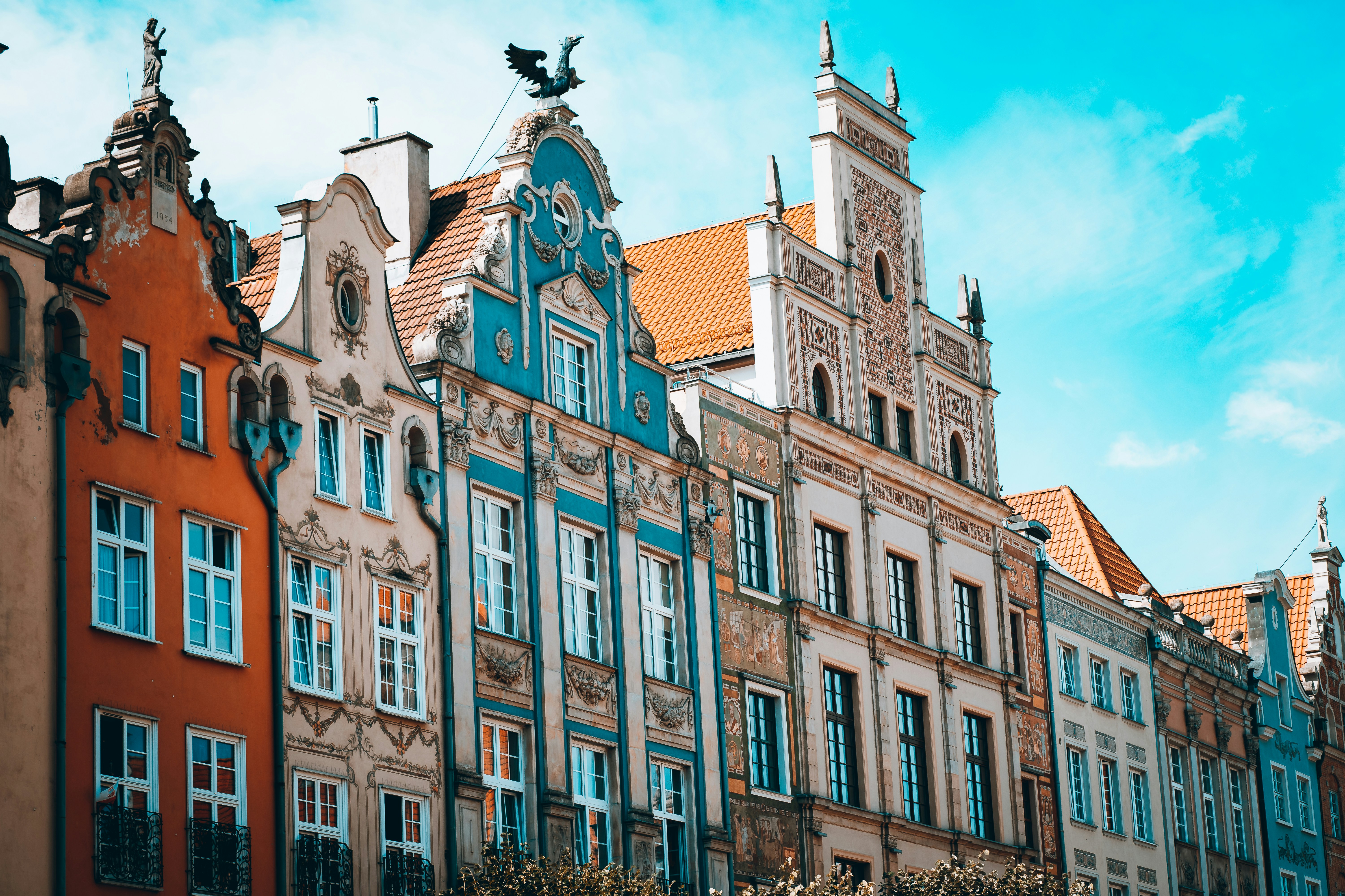 Colorful historic buildings line a street in Gdańsk, showcasing intricate architectural details and vibrant hues.