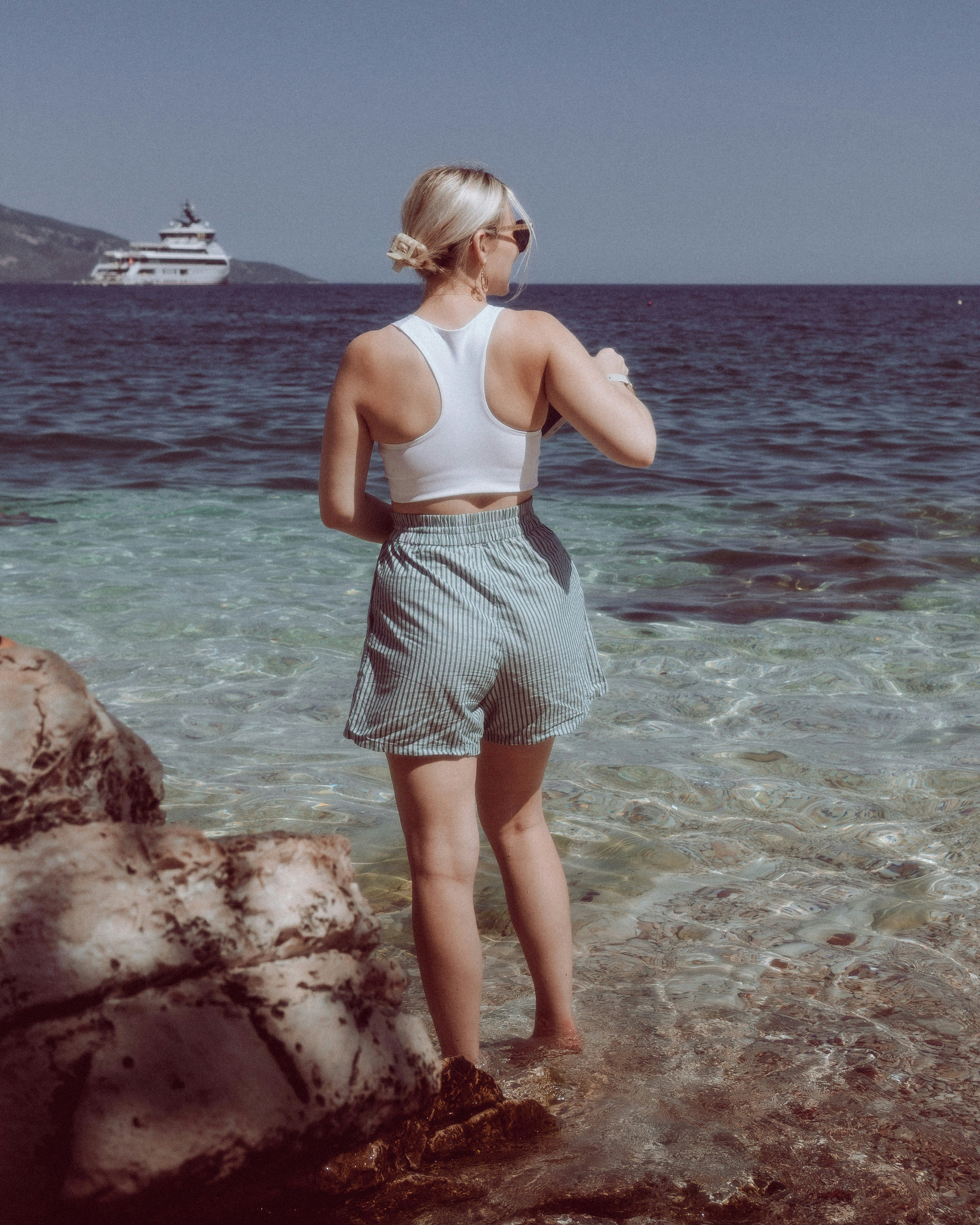 Sunlit Shoreline Portrait: Woman in White Top by the Sea