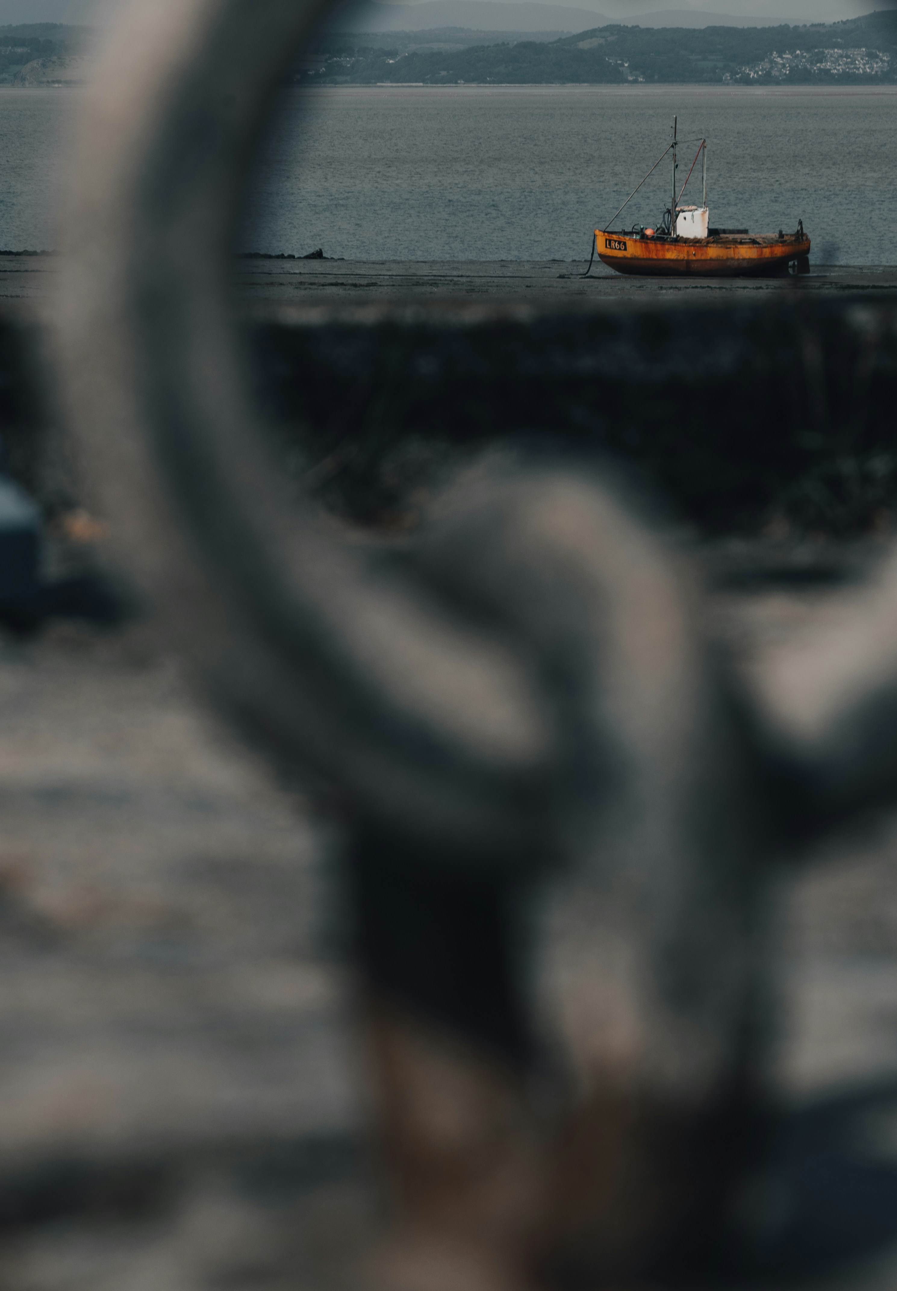 An old fishing boat anchored in the calm waters, framed by a blurred foreground element, suggesting a sense of nostalgia and tranquility.