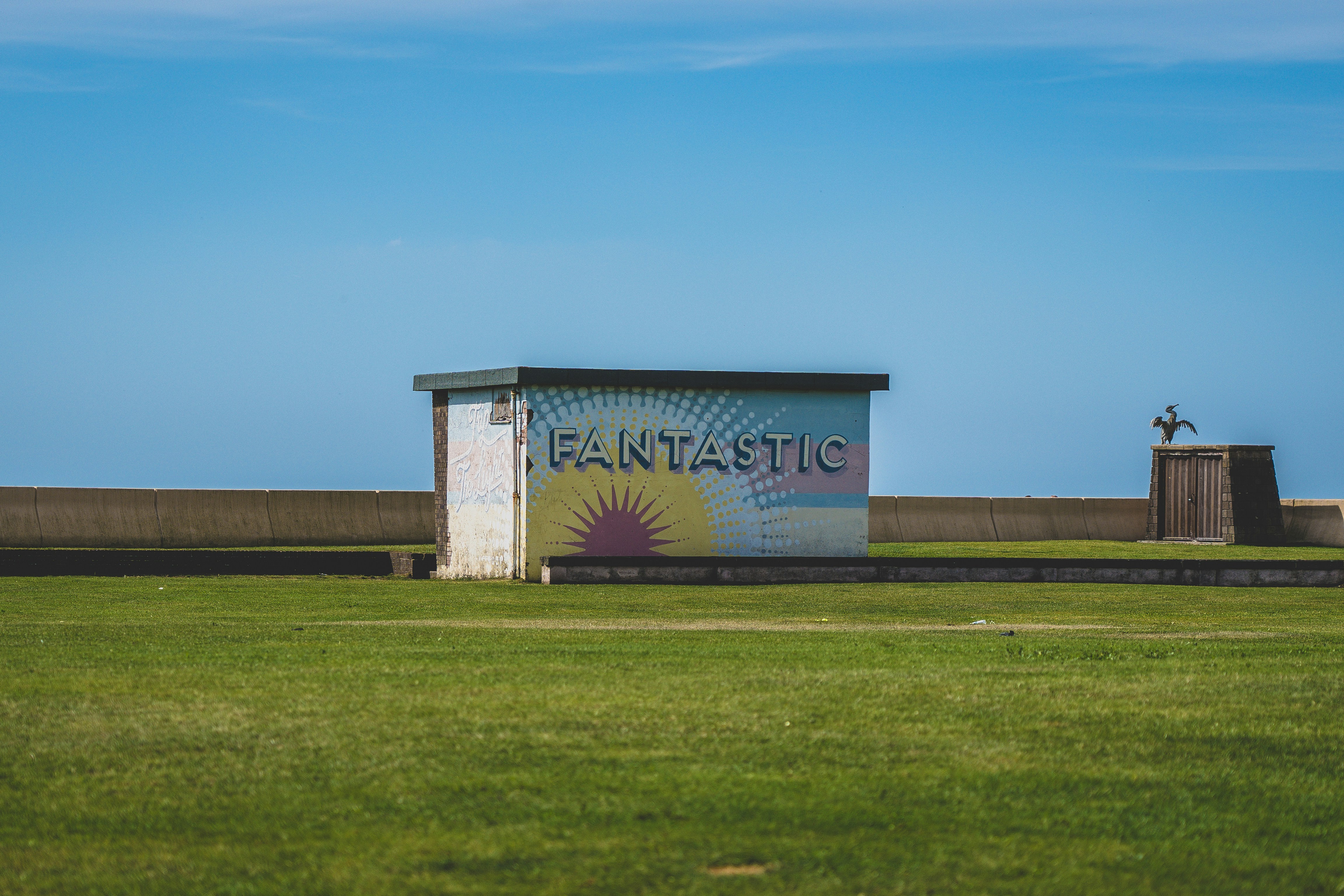 Small building with graffiti in a grassy field near the coast under a clear blue sky.
