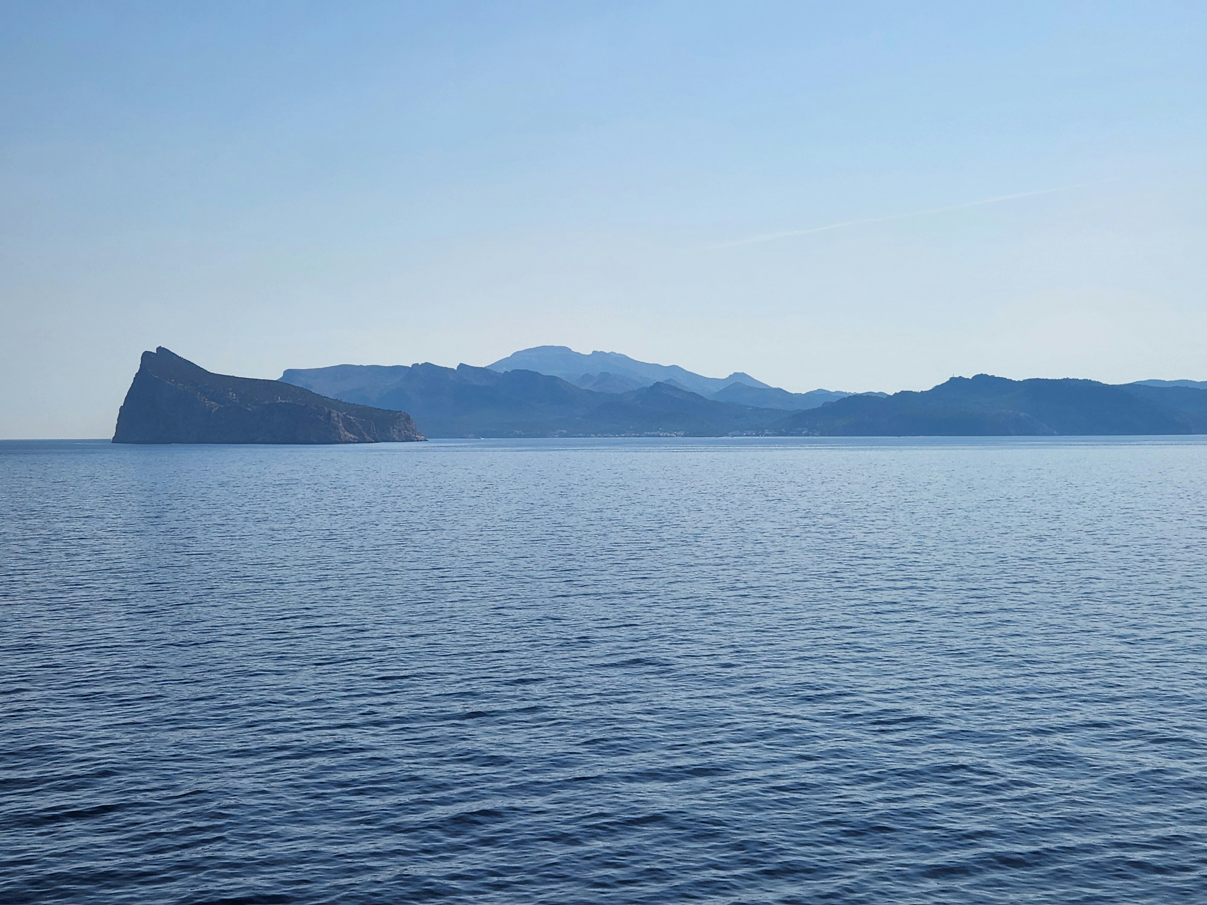 Distant coastal landscape featuring a prominent rocky outcrop against a tranquil sea and clear sky.