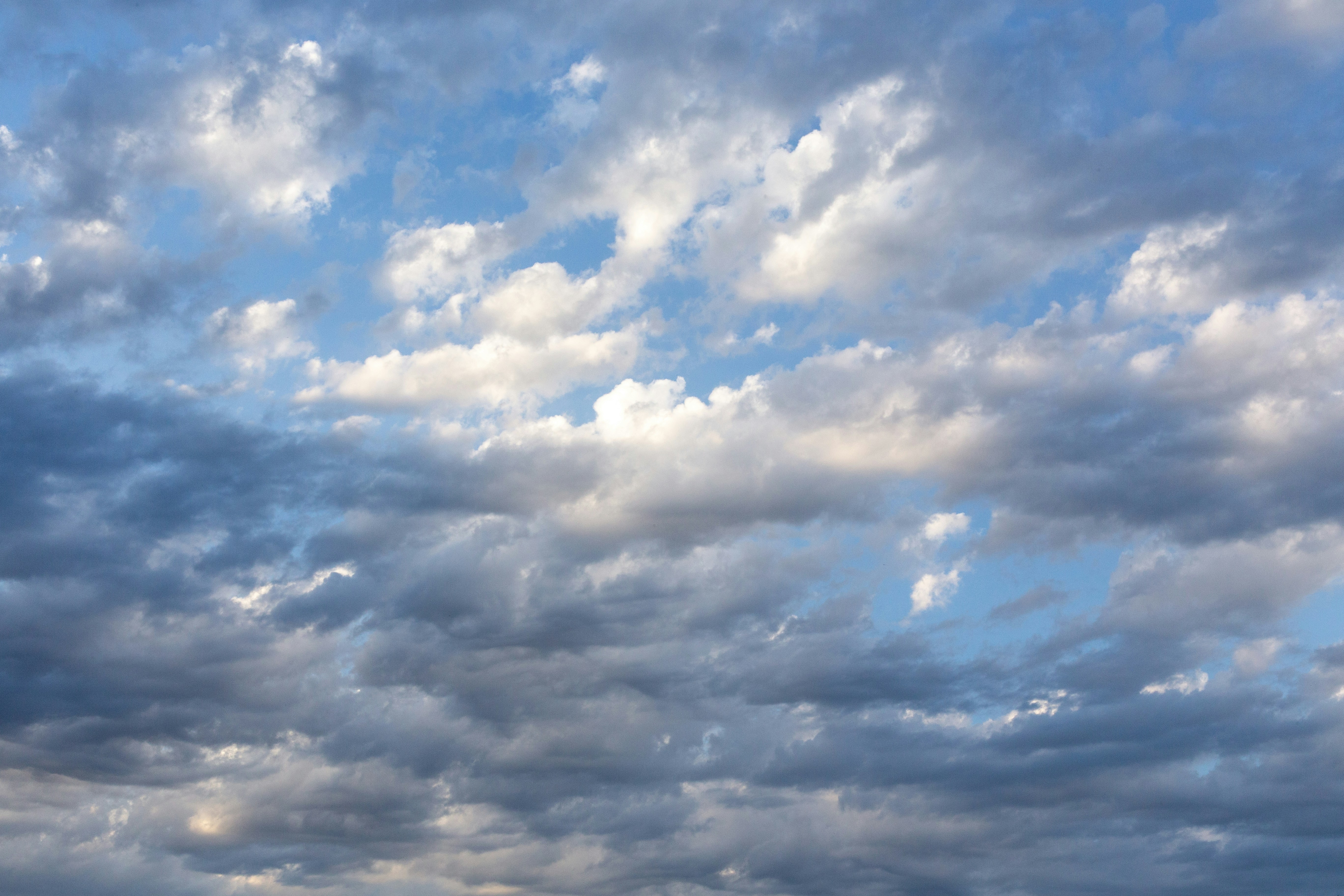 A sweeping view of a dynamic cloudscape, showcasing a blend of light and shadow across the sky. The clouds create an atmospheric tapestry of varying shades.