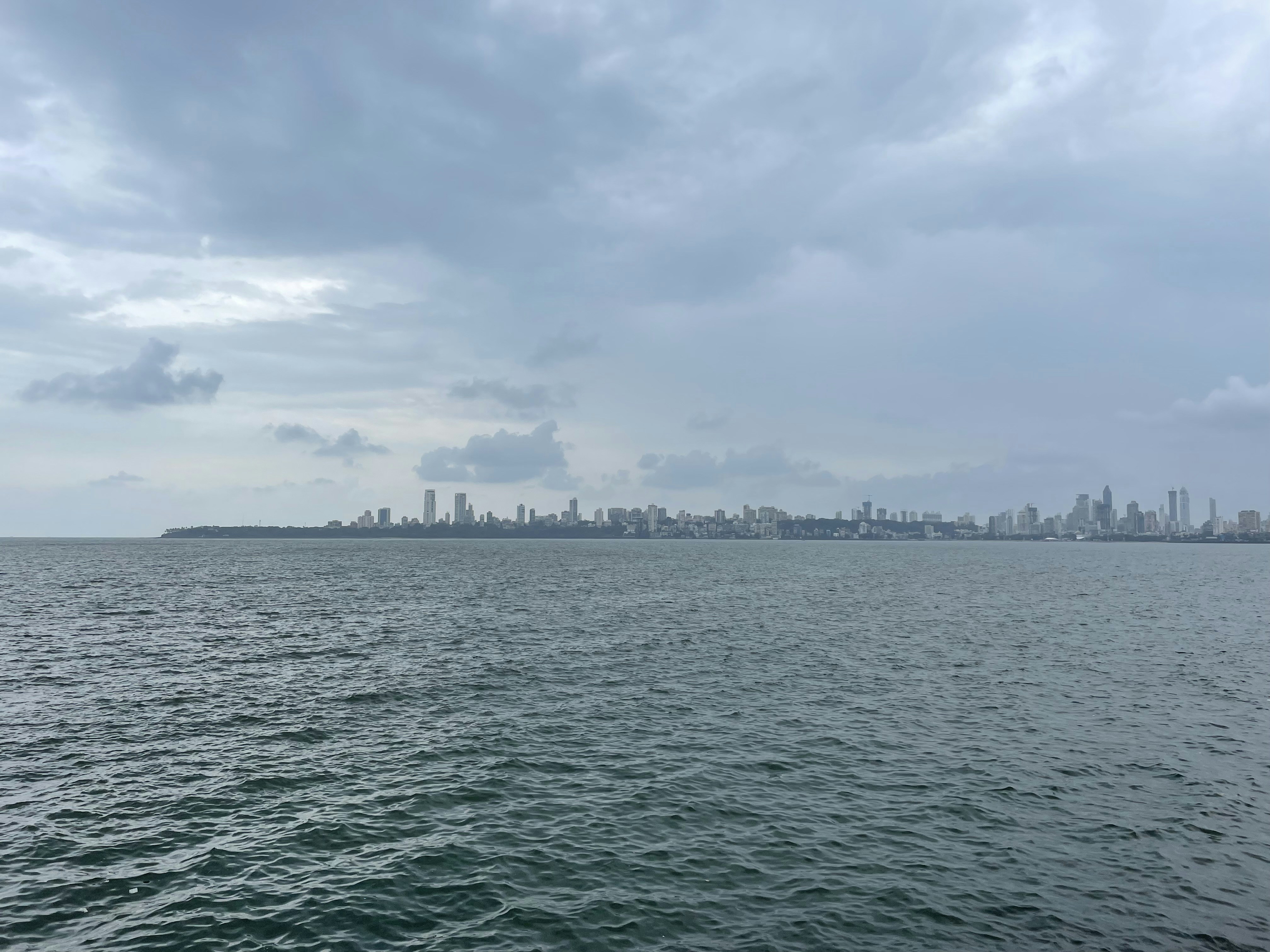 A coastal view showcasing a sprawling city skyline under an overcast sky, with gentle waves in the foreground.