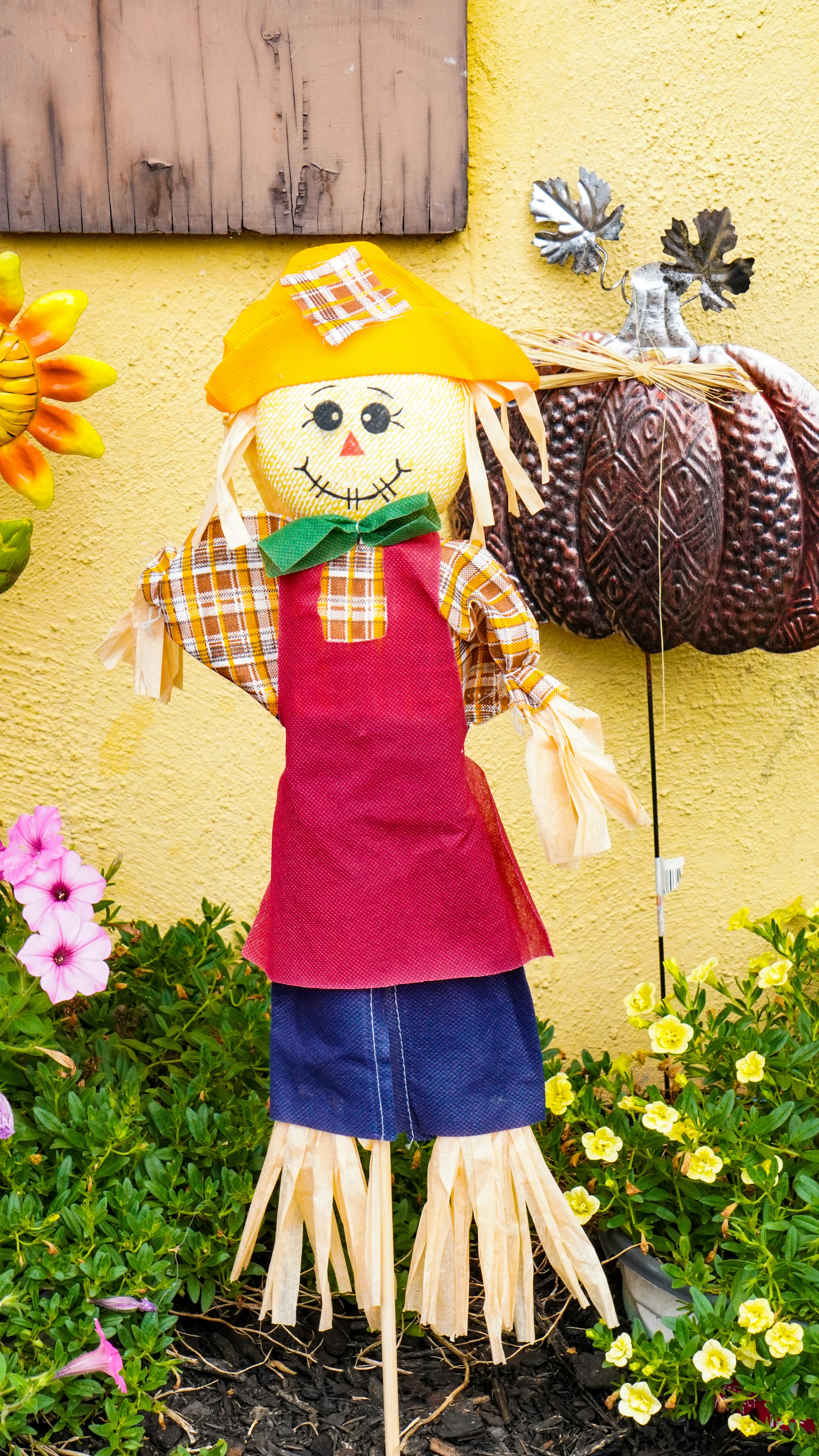 Sunny Harvest Smile: A Festive Scarecrow Standalone in a Flower Bed