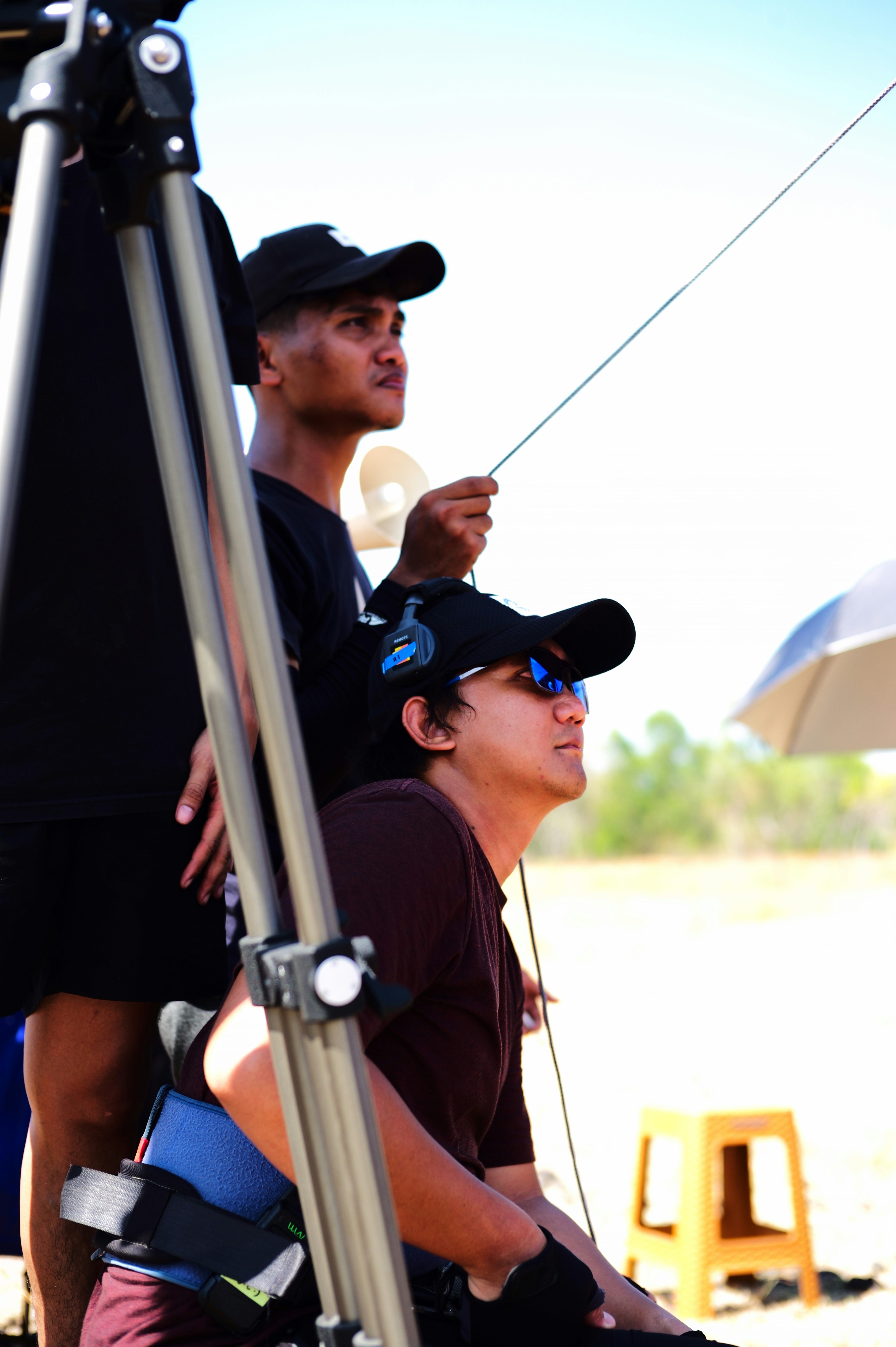 Line of Sight: Two Crew Members Steady by a Towering Tripod on a Bright Set