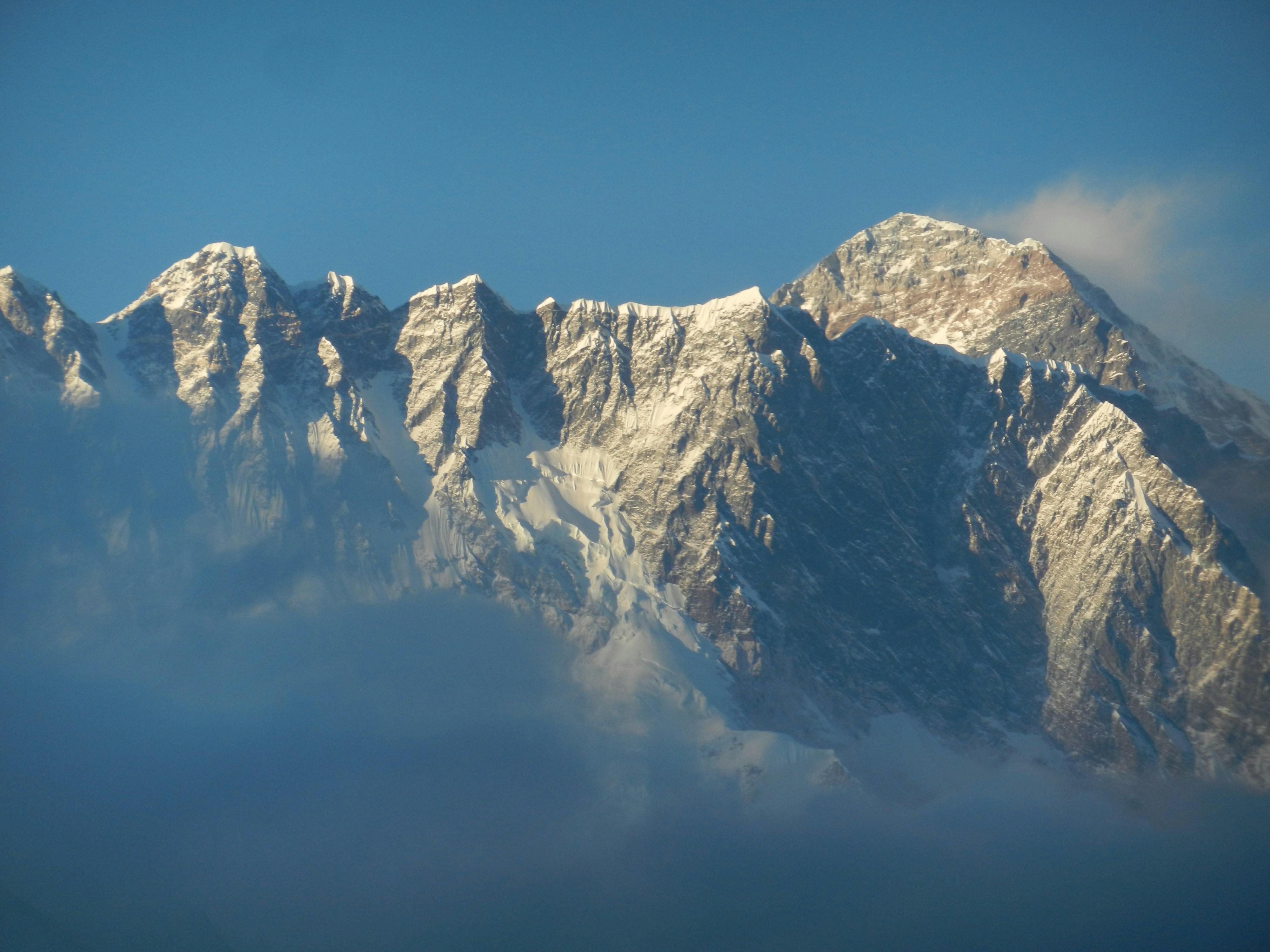 Majestic snow-capped mountain range emerging from a blanket of clouds under a clear blue sky.