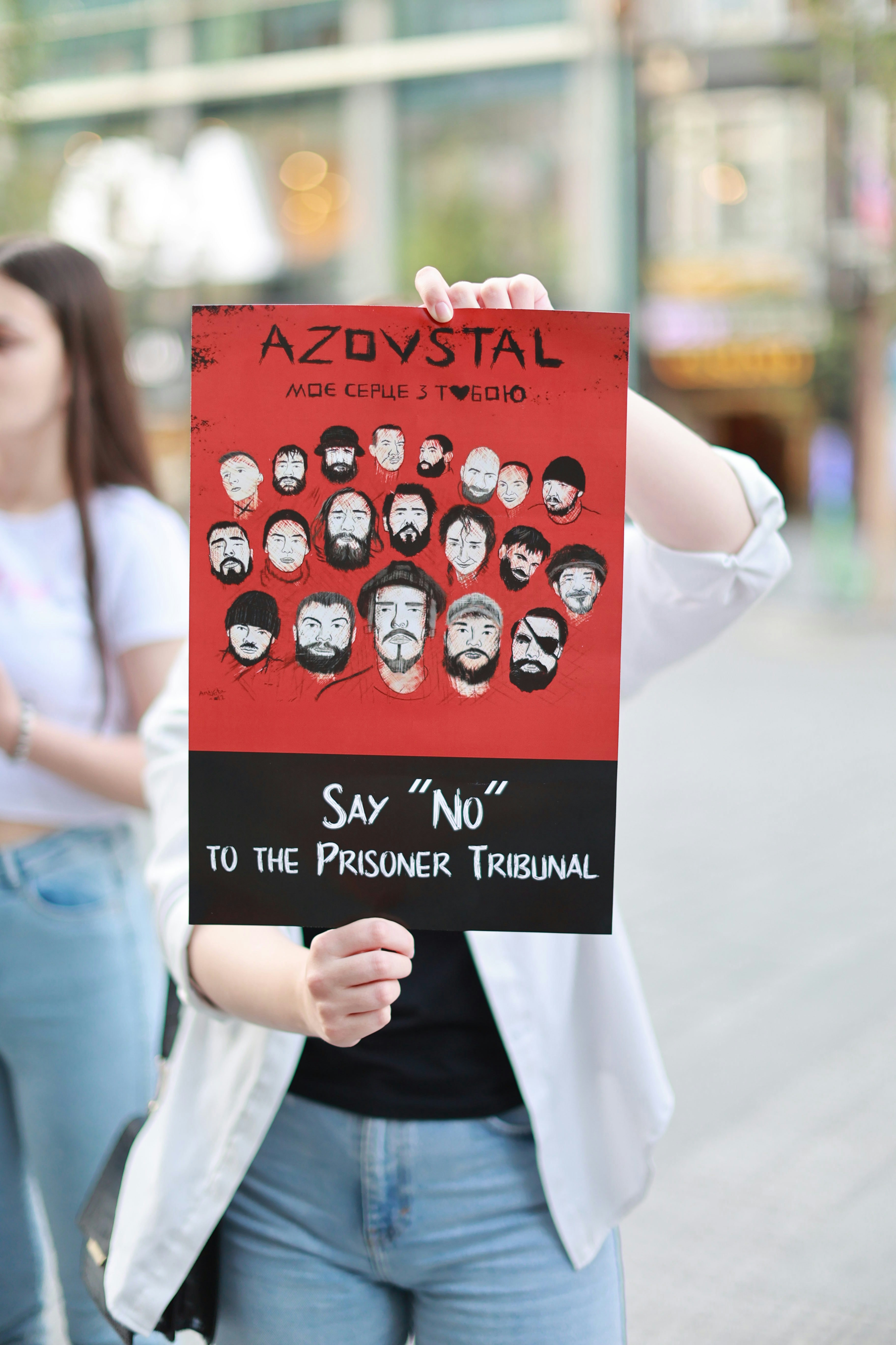 Protester holding a sign featuring portraits of individuals from Azovstal, advocating against the prisoner tribunal.
