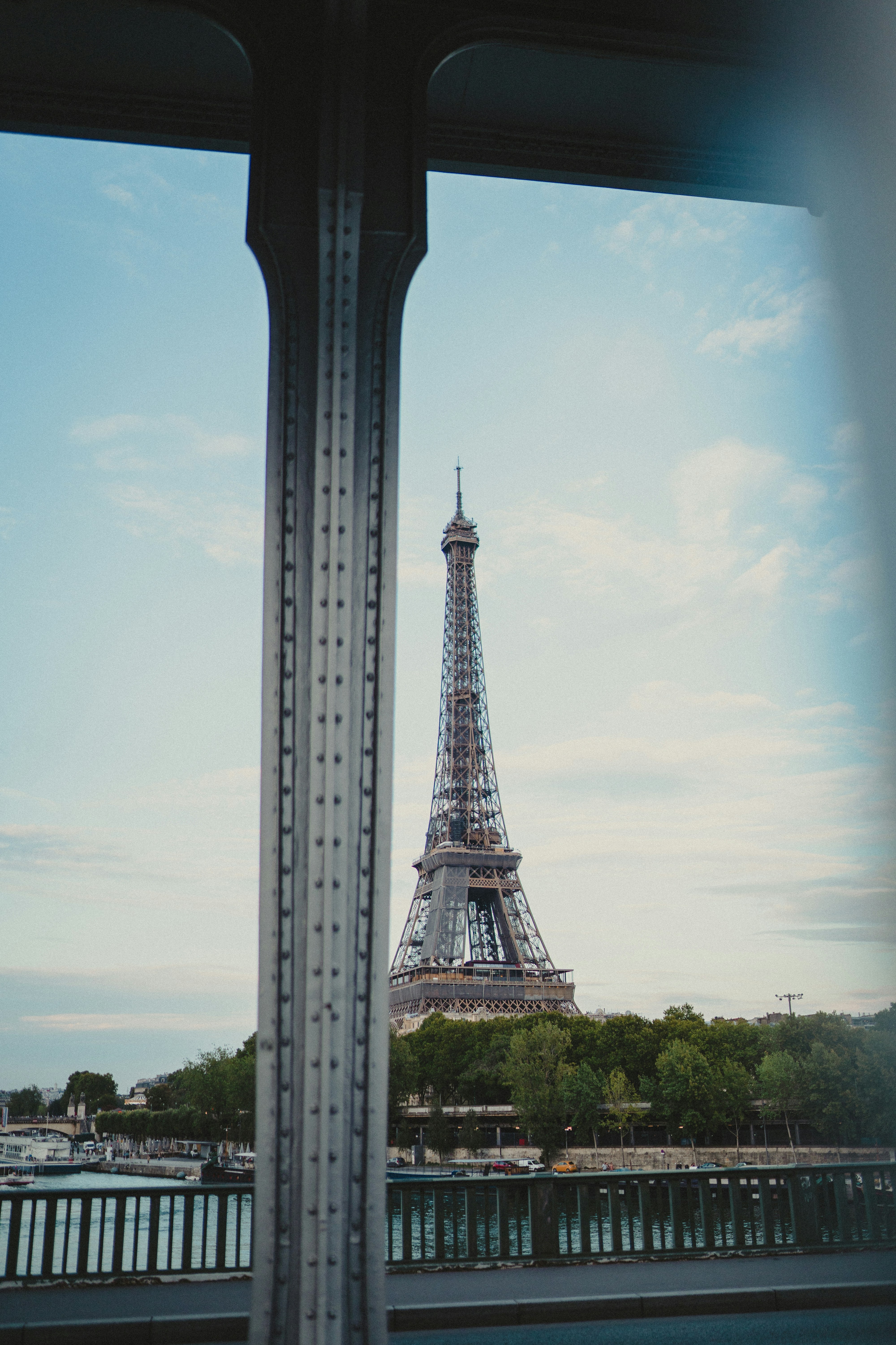 Eiffel Tower framed by the intricate ironwork of a bridge, showcasing the blend of architectural elegance and natural beauty.