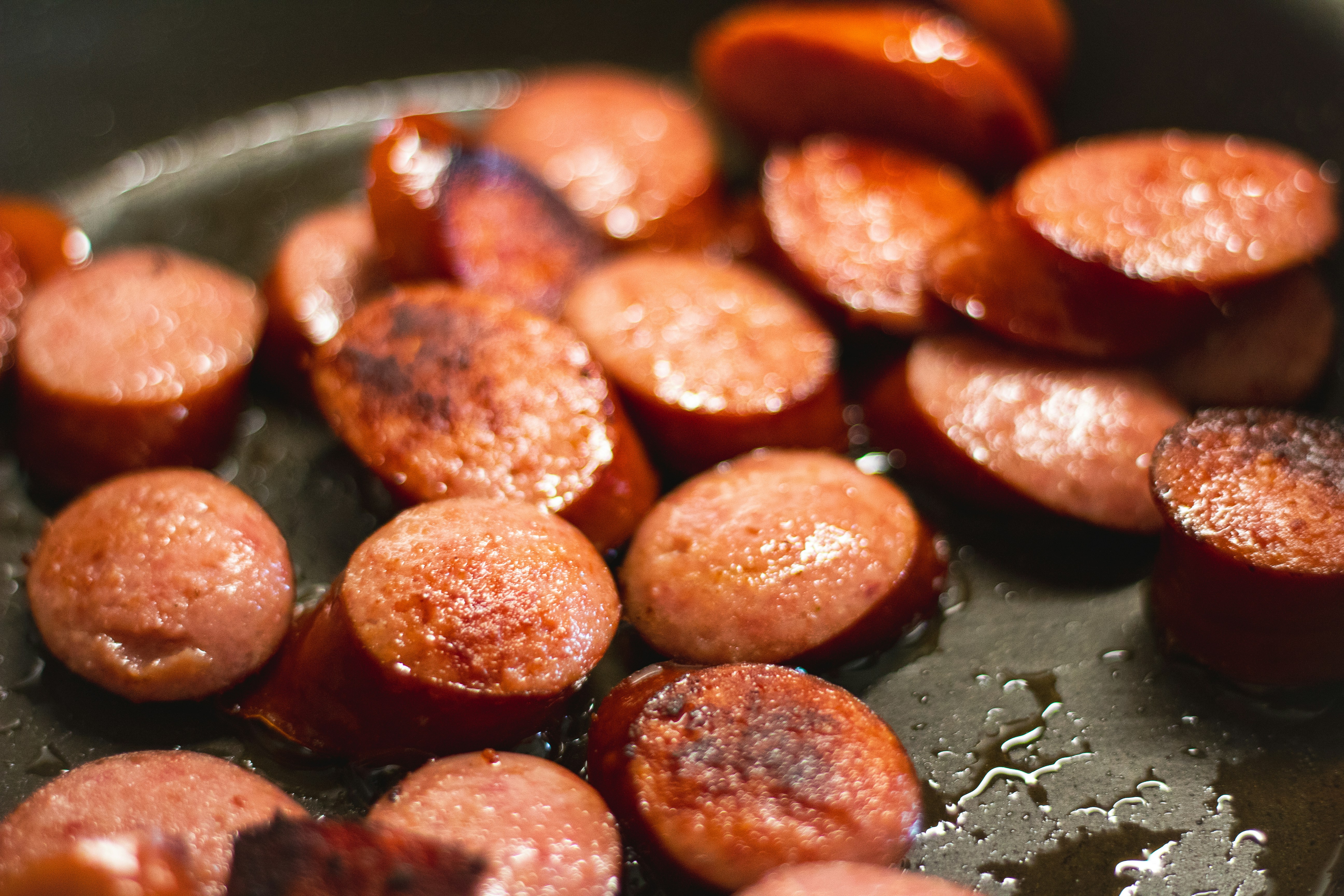 Close-up of sliced sausages sizzling in a skillet, showcasing their golden-brown edges and glistening surface. Perfect for a hearty meal.