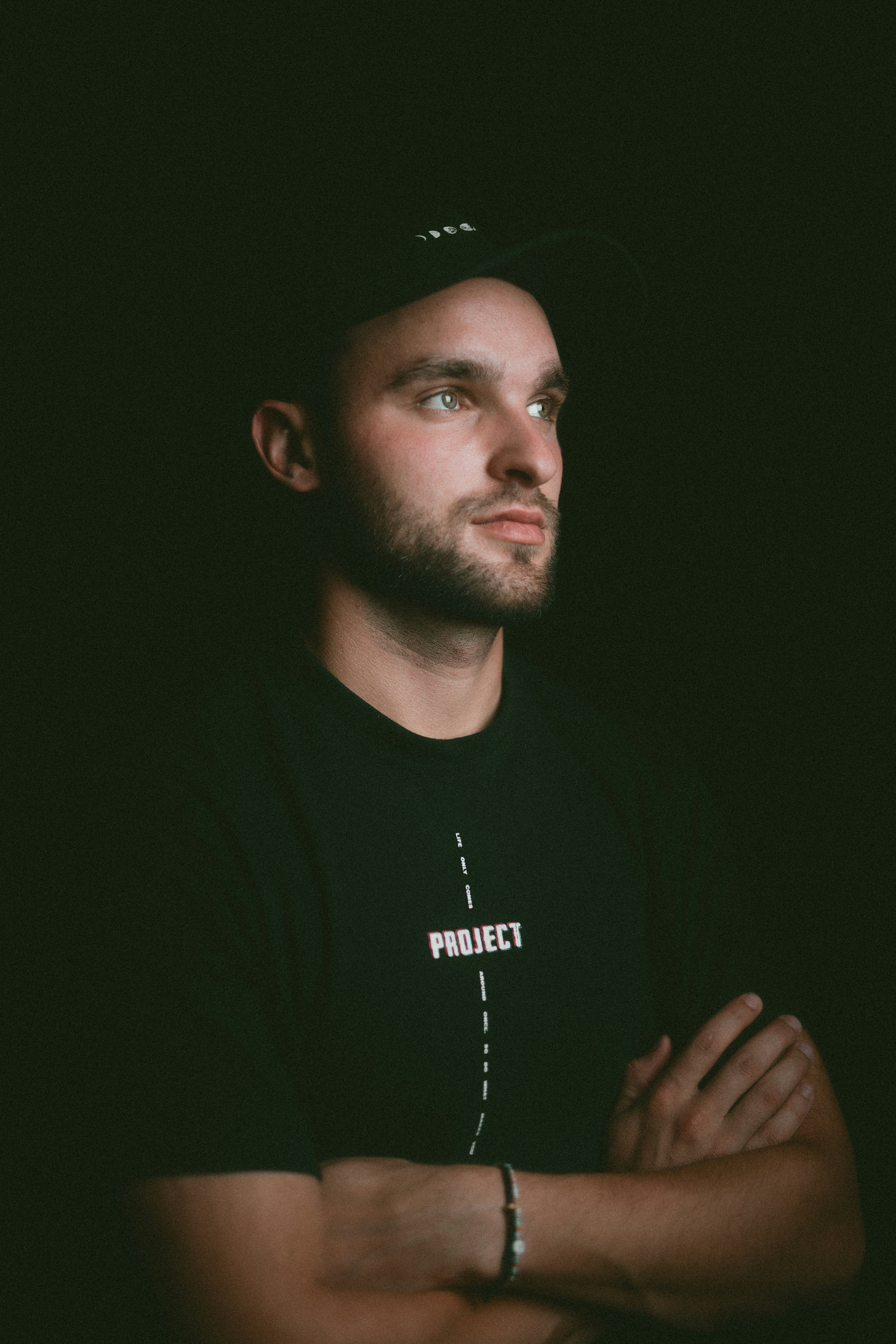 Man with crossed arms gazing into the distance against a dark background.