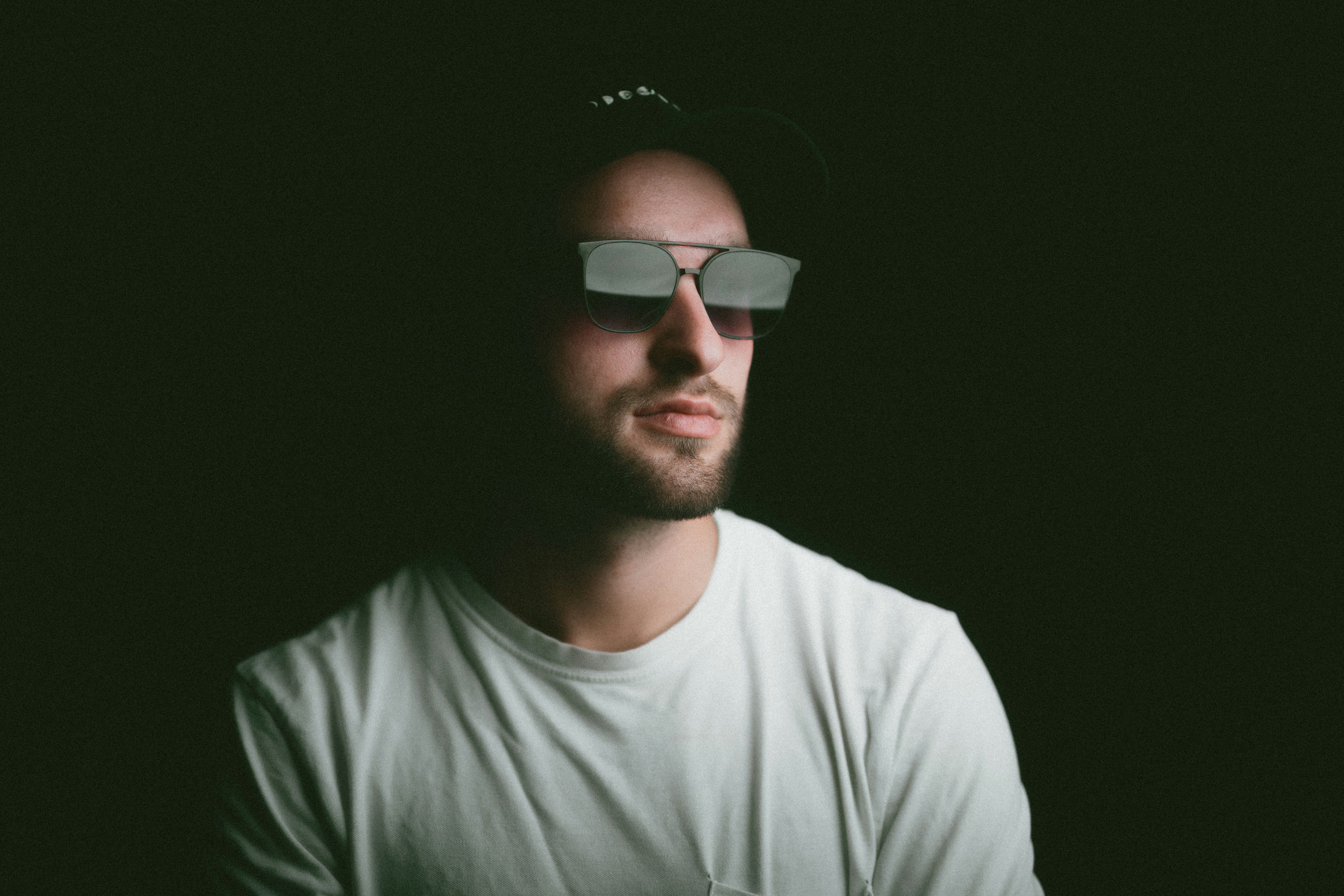 Person wearing sunglasses and a cap against a dark background.