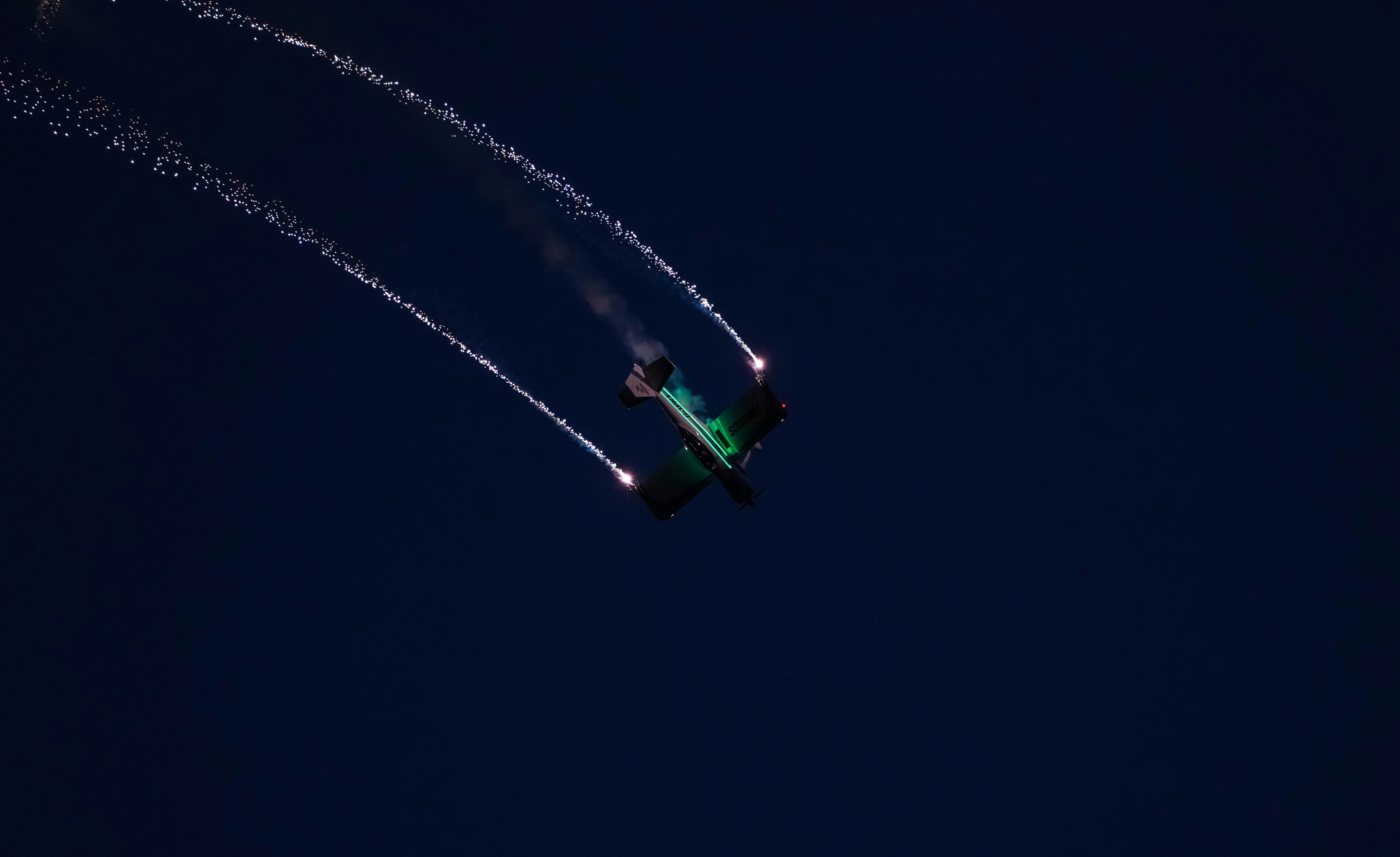 Acrobatic aircraft performing a dazzling display against a twilight sky, leaving trails of sparkling light.