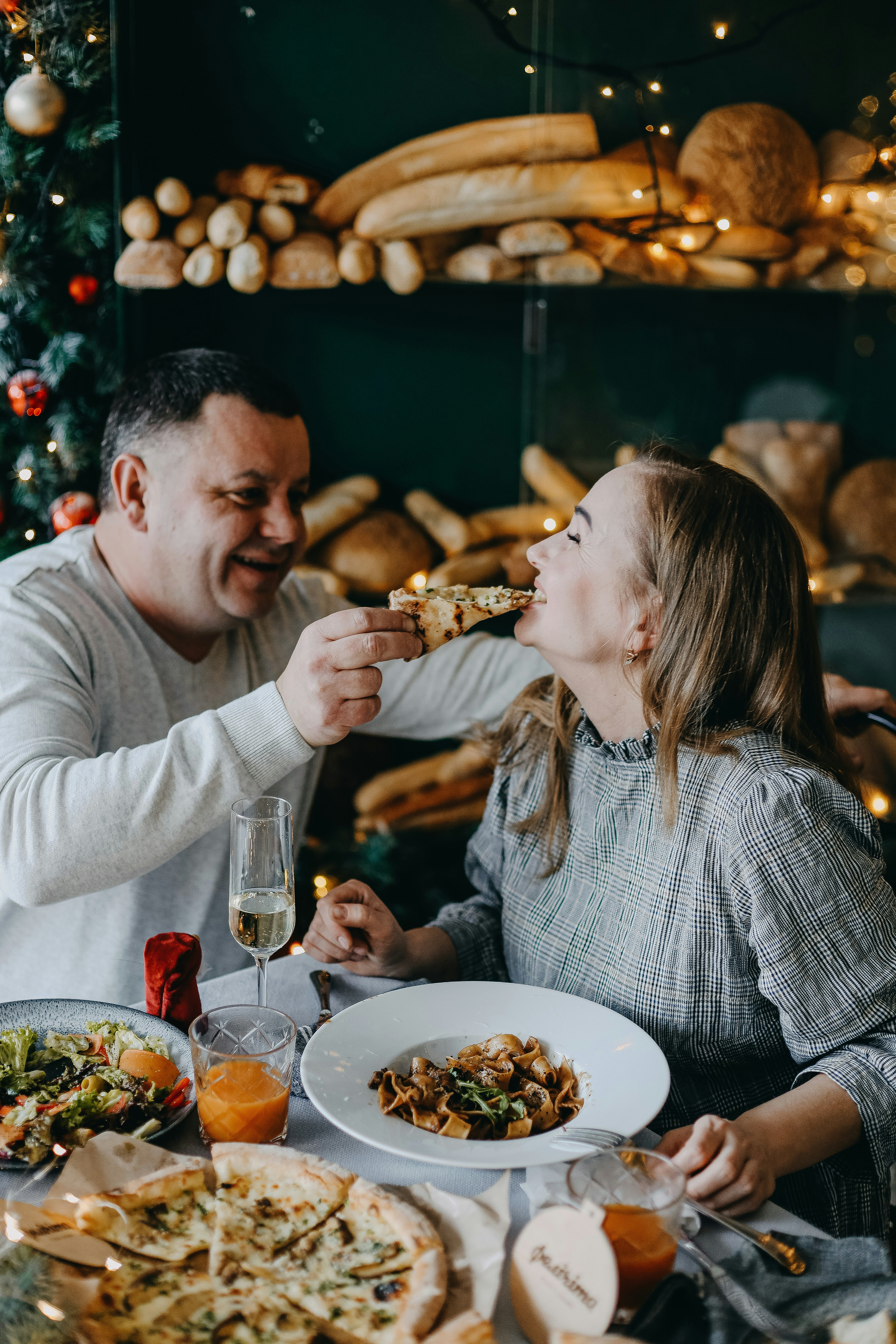 Couple enjoying a meal together with festive decorations and bread display in the background.