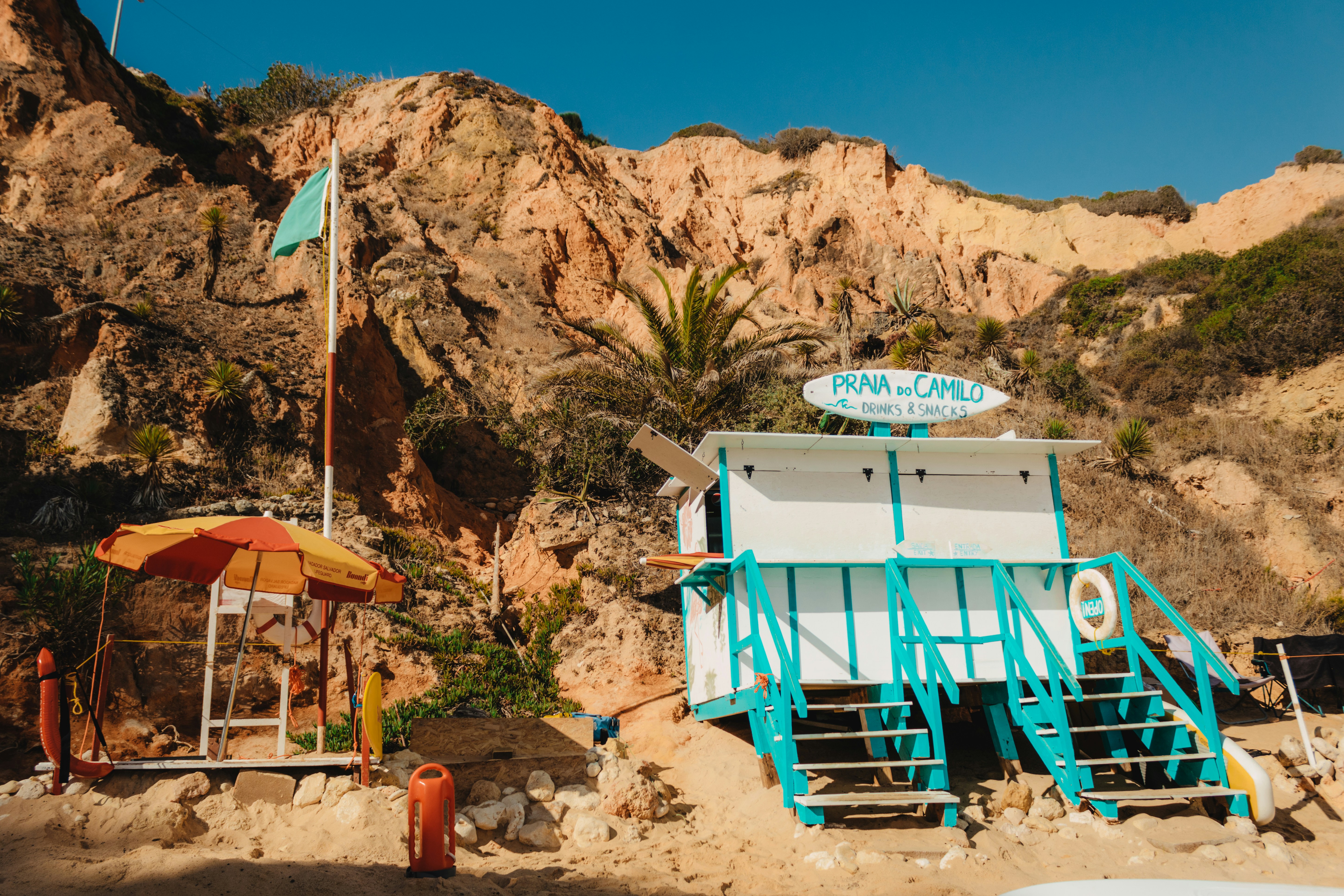Lifeguard hut and umbrella set against rugged cliffs under a clear blue sky.