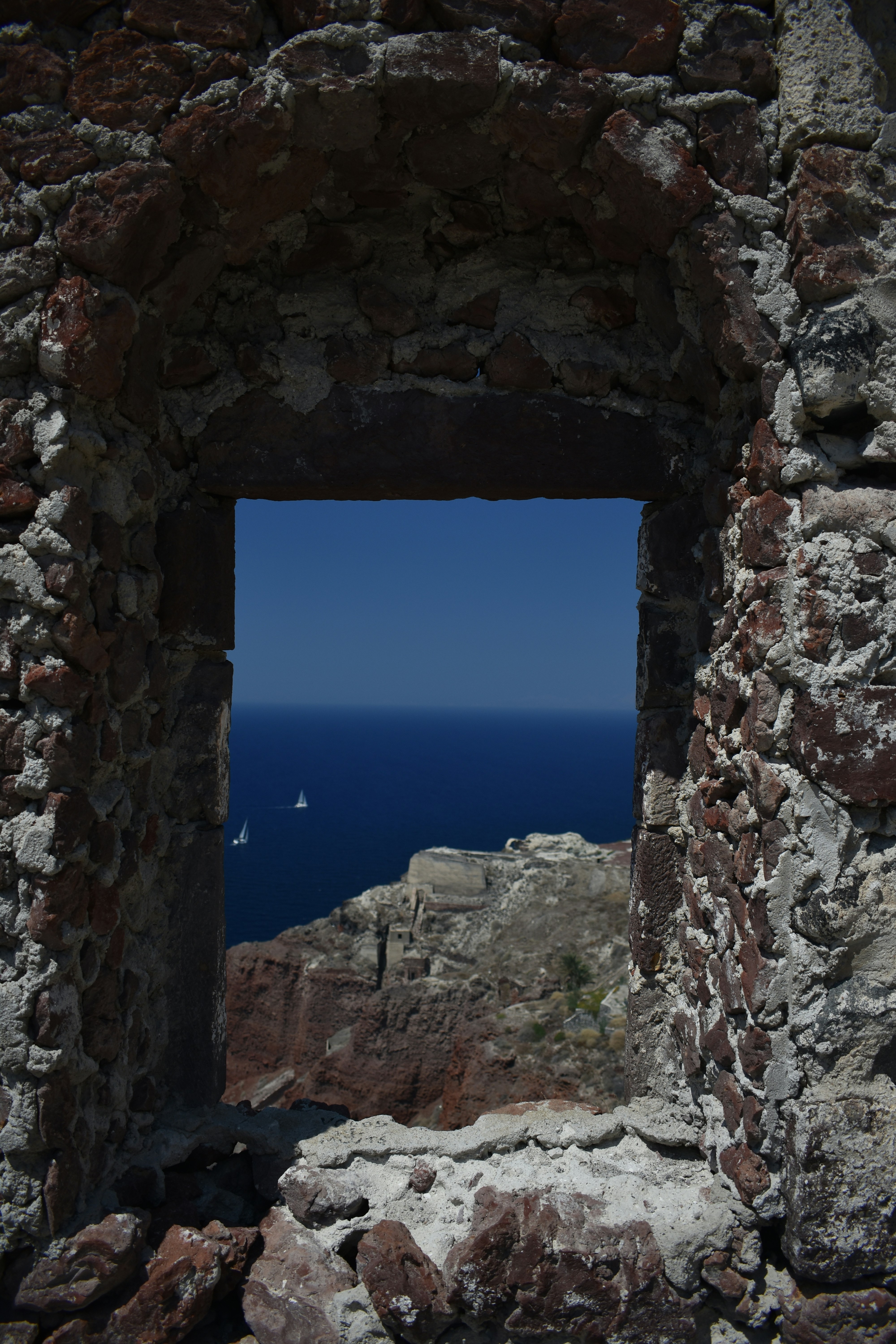 Horizon Through a Weathered Window: Sailboats Beyond a Cliffside Ruin