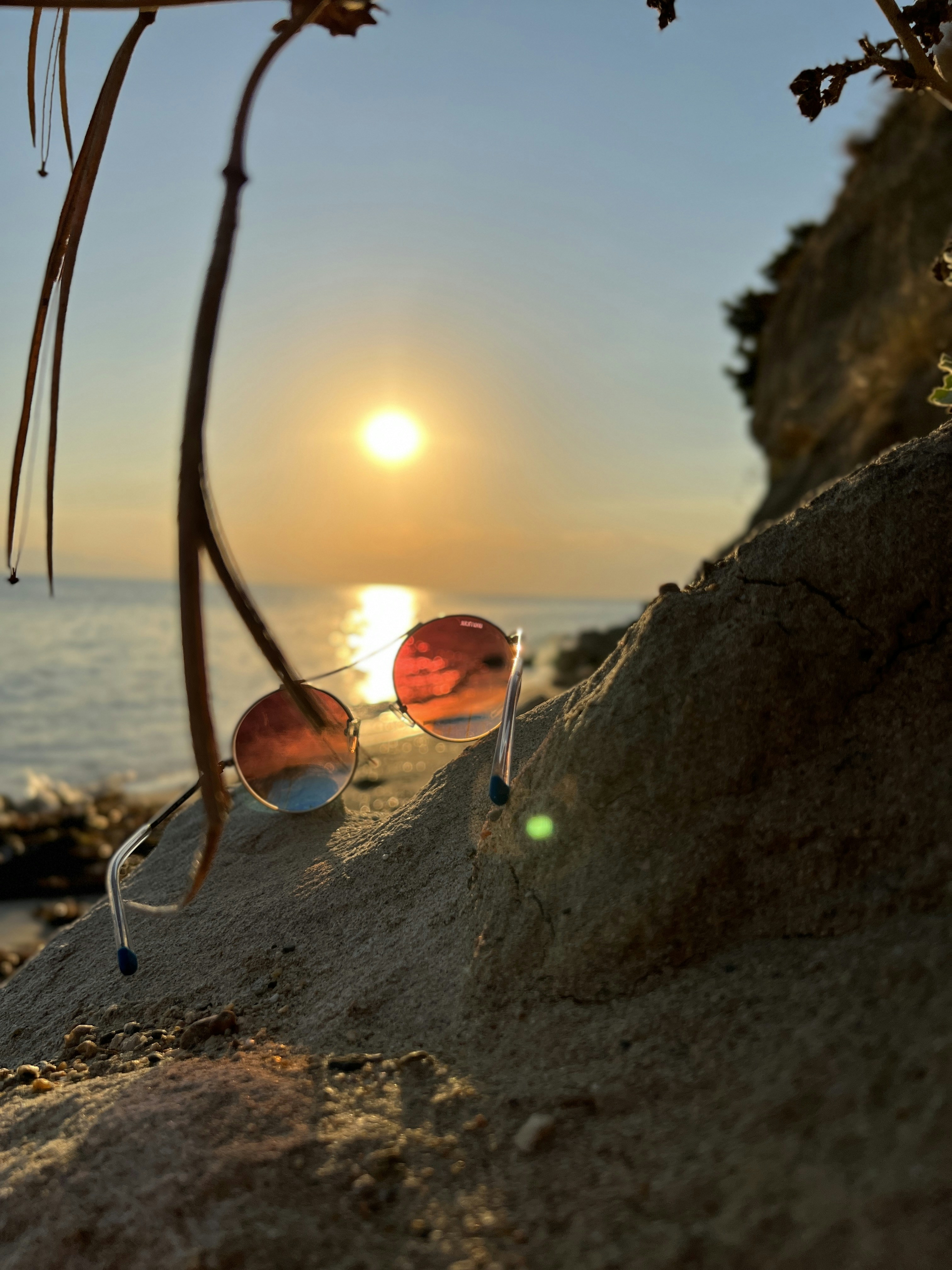 Round sunglasses on a sandy beach capturing a vibrant sunset over the ocean.