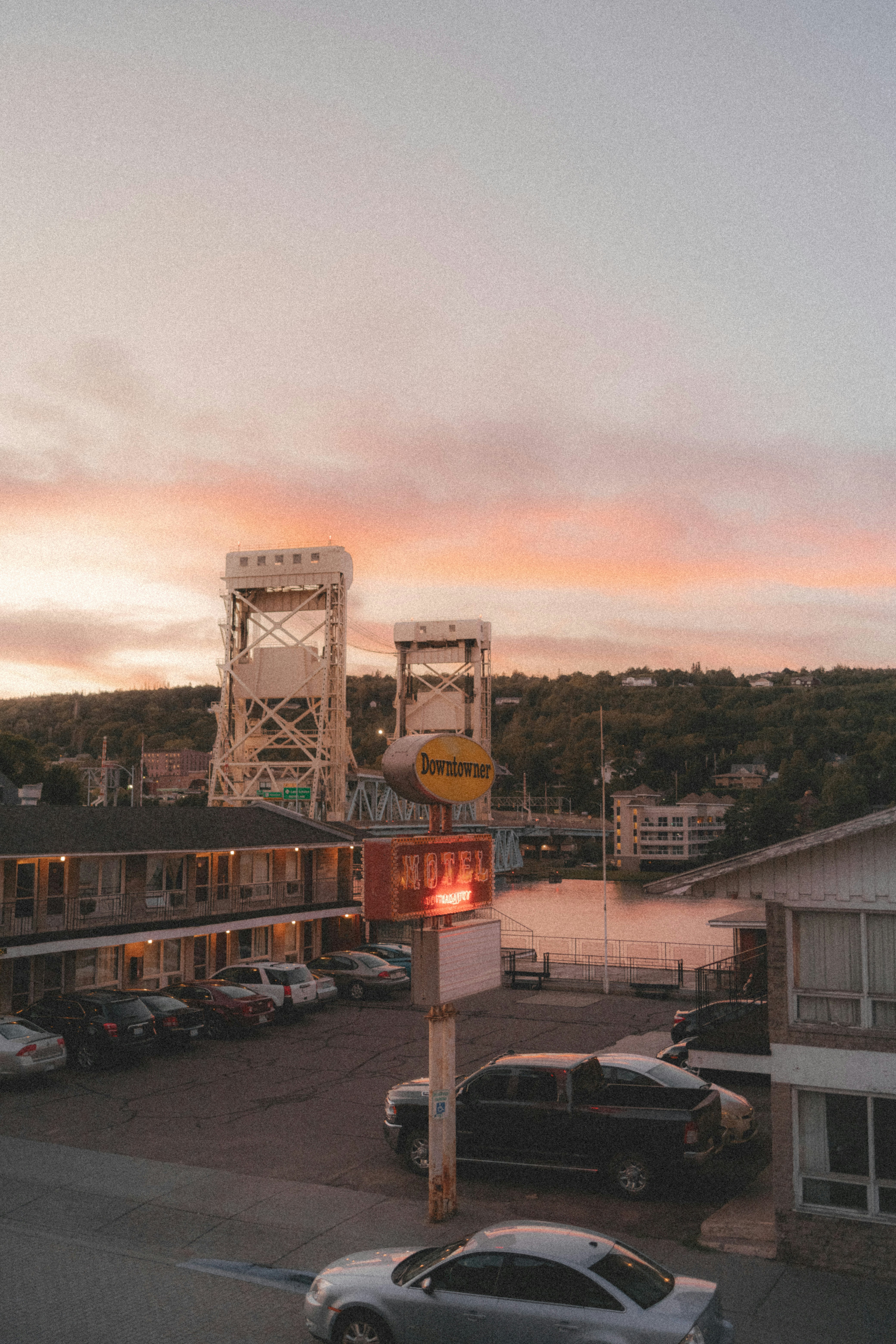 Historic lift bridge towers above a peaceful waterfront, framed by a quaint motel and vibrant sunset hues.