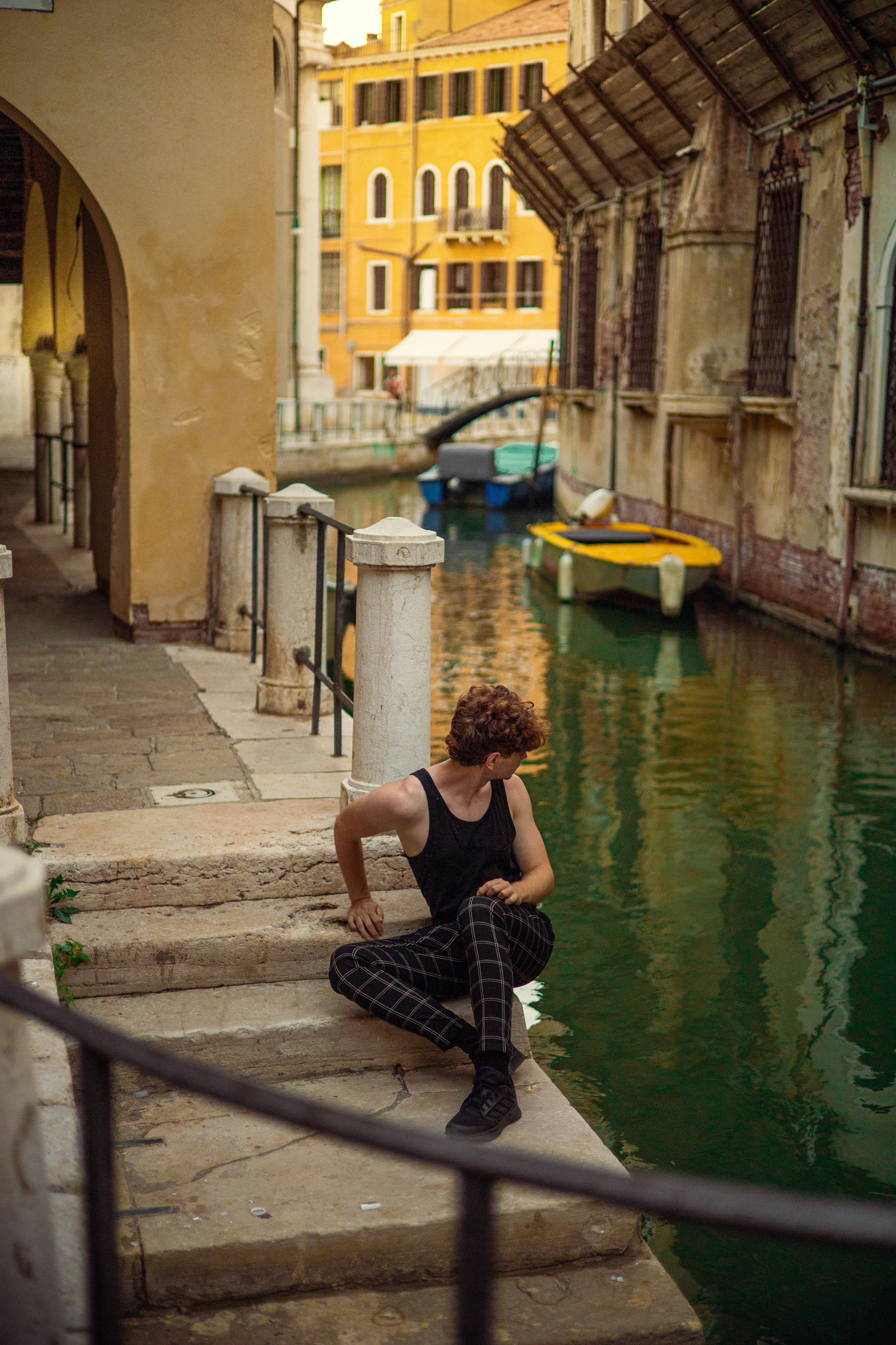 Sunlit Venice: a solitary figure perched on canal stairs beside emerald water