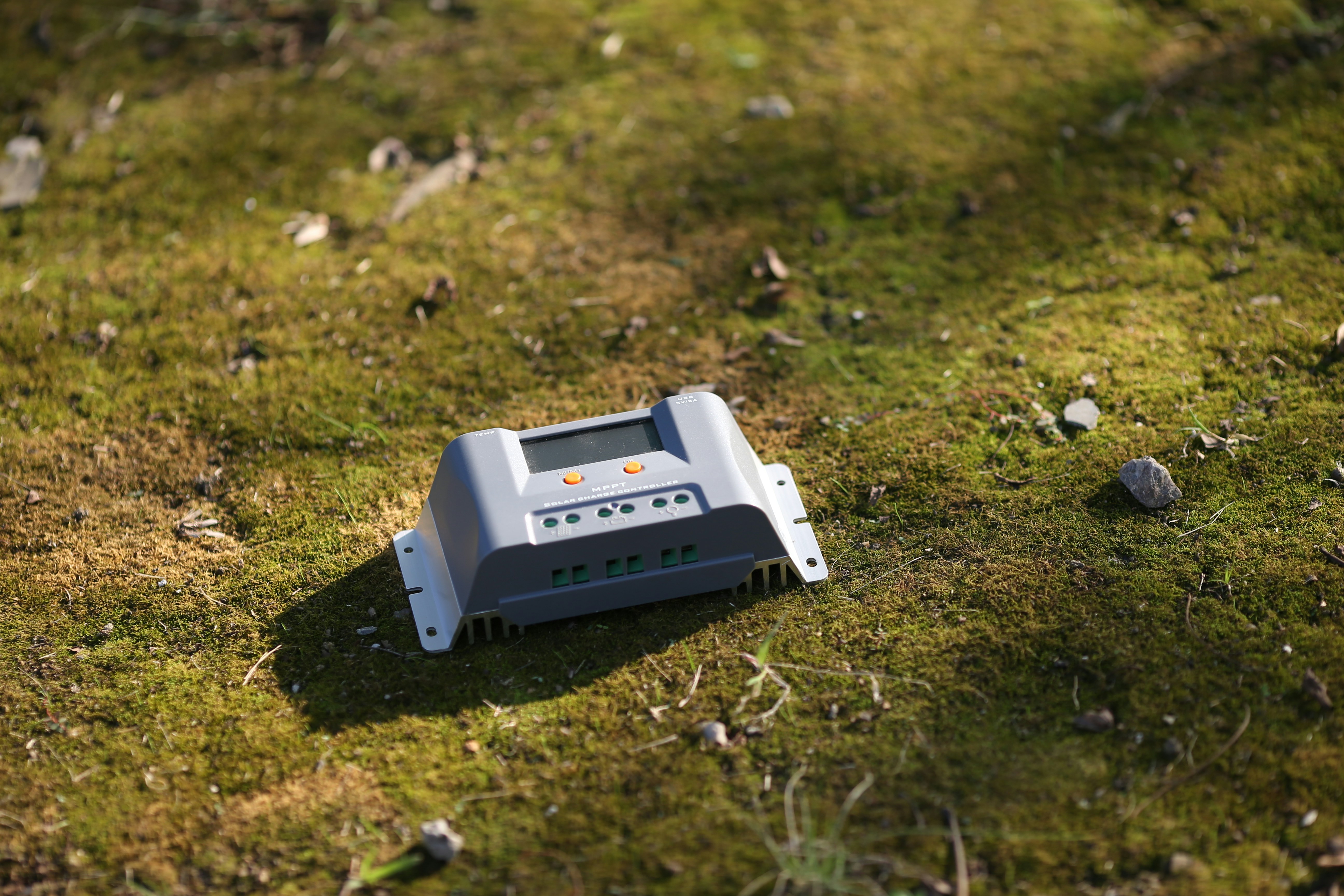 A compact rugged electronics module rests on sun-dappled moss
