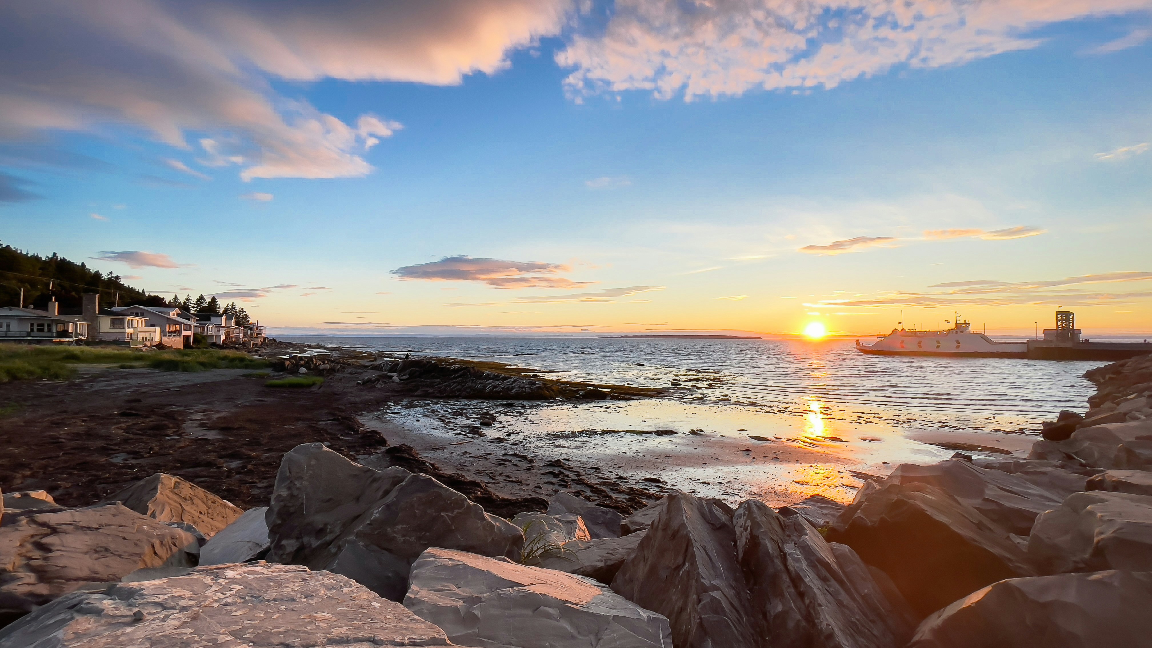 Sunset casting vibrant colors over the rocky shore of St-Lawrence River, with clouds scattered across the sky.