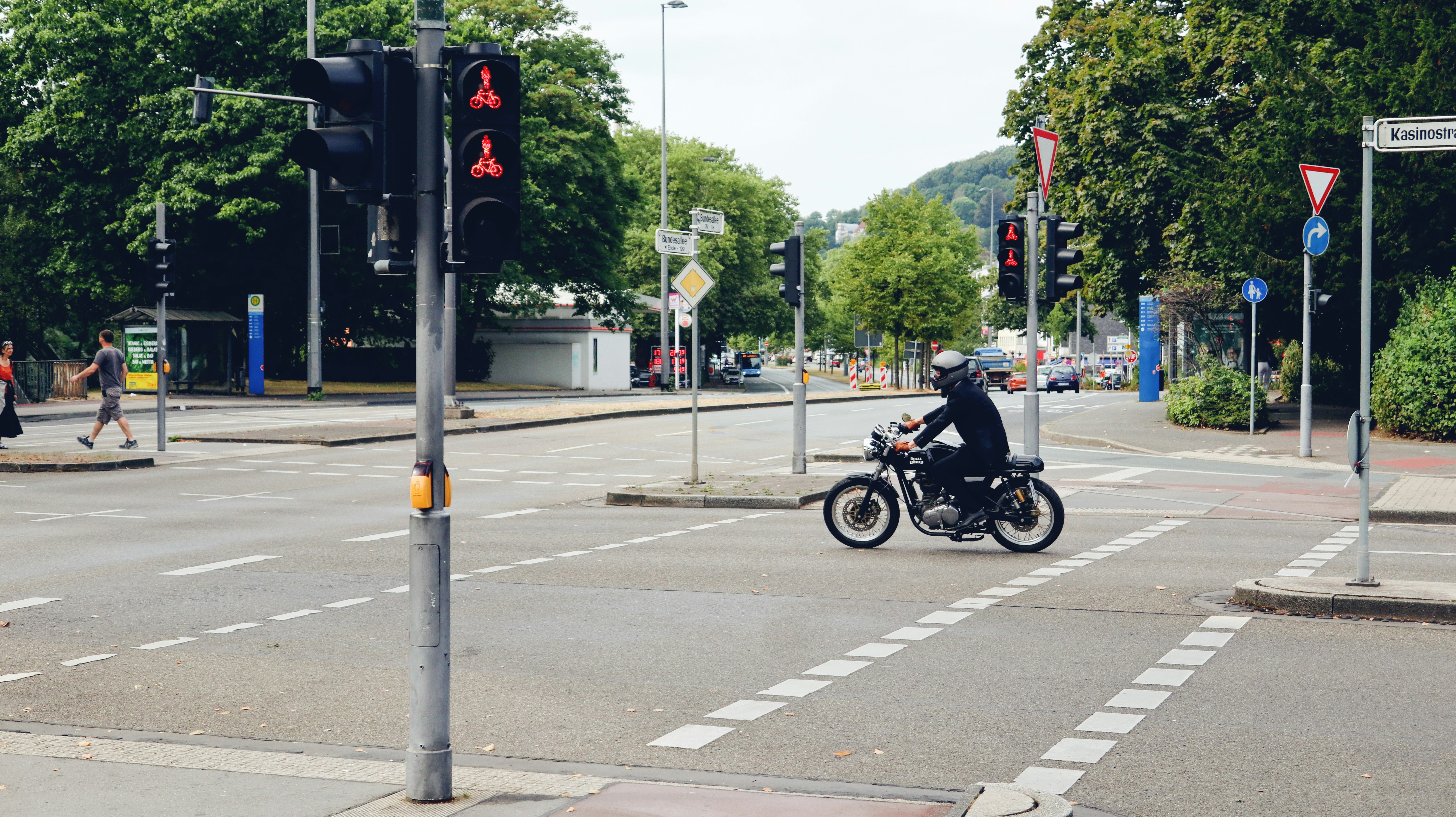 Motorcyclist navigating an urban intersection with traffic lights and pedestrians in the background.
