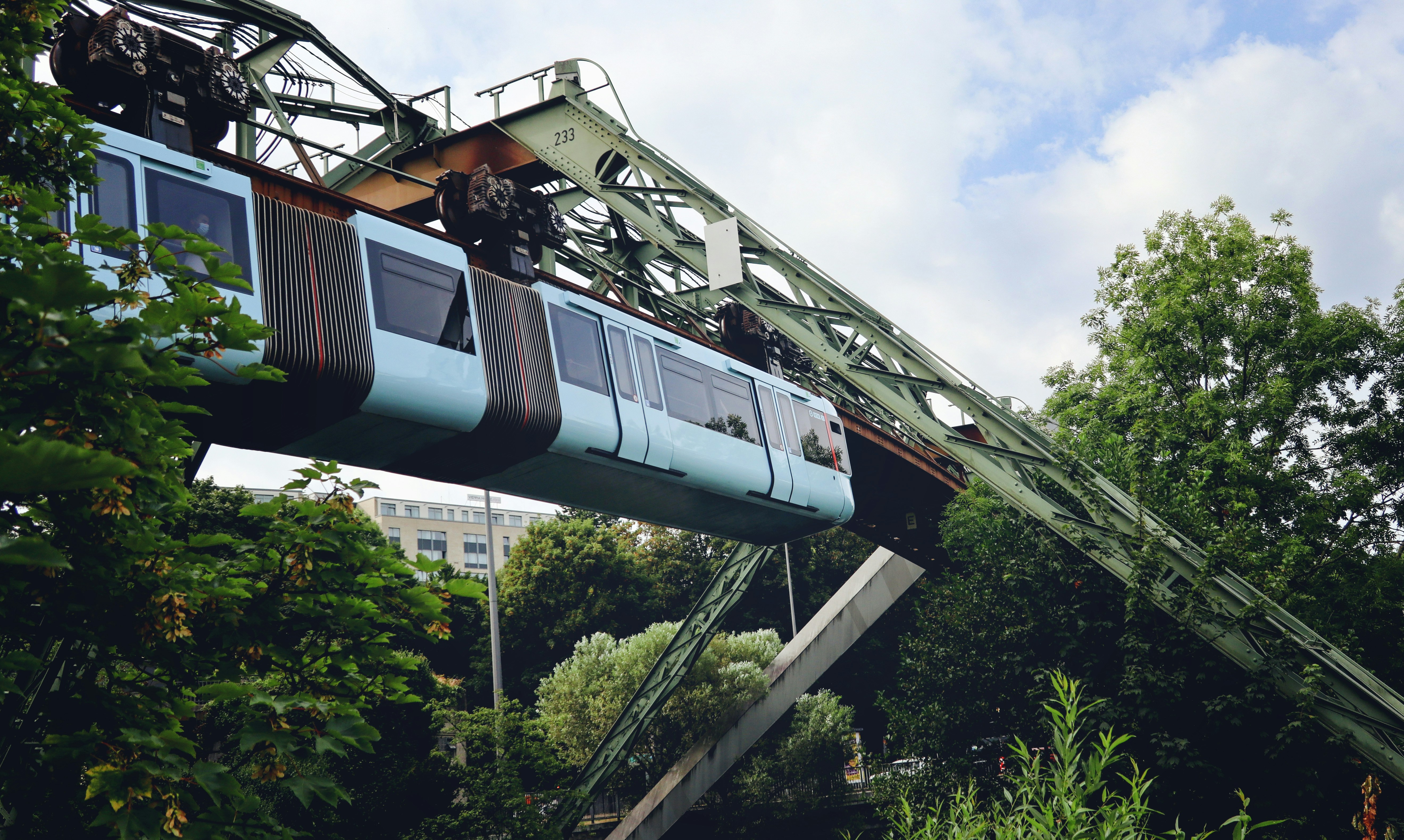 Blue Passenger Car Perched on a Verdant Green Arch Above Tree-Lined Terrain