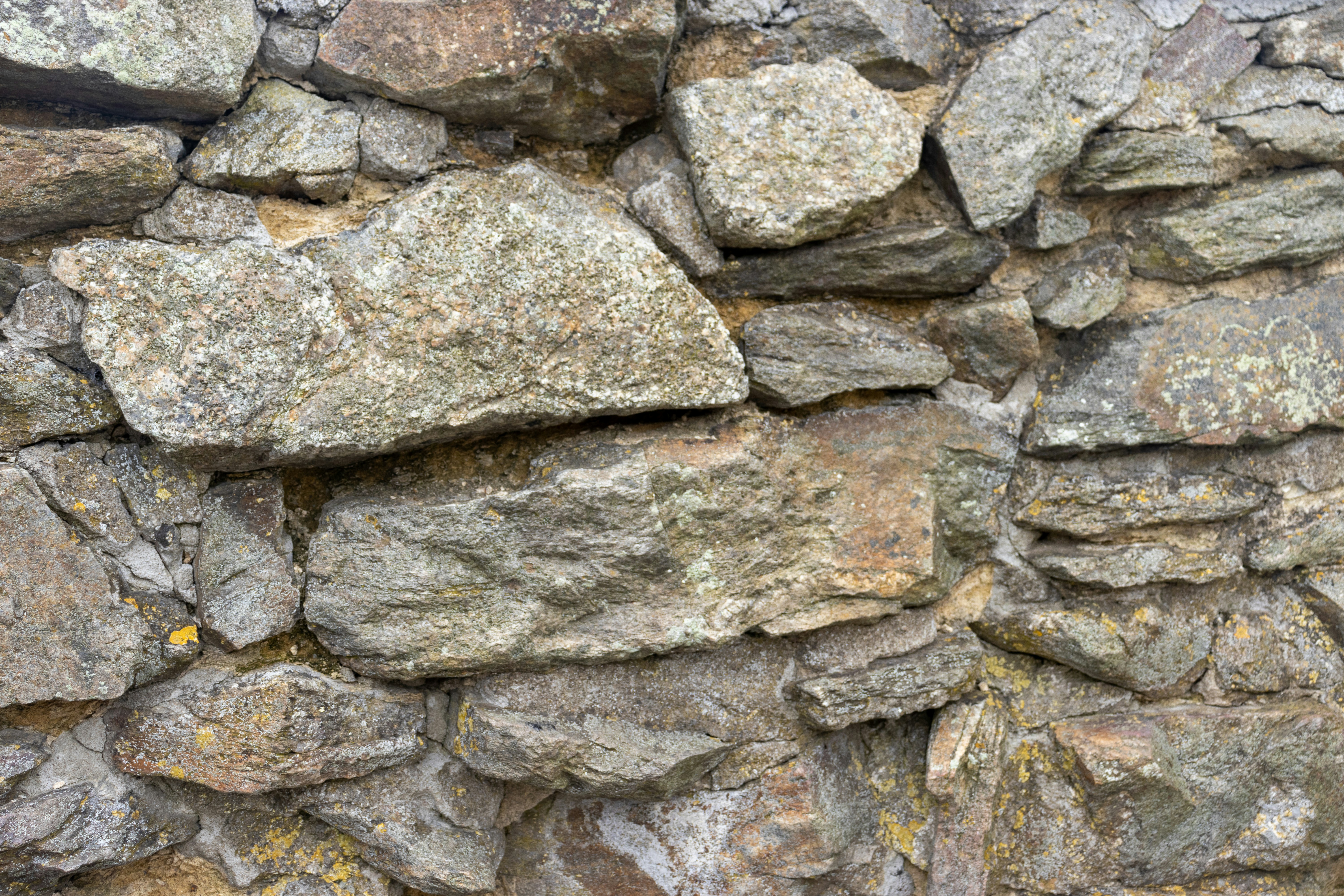 Close-up of a rugged stone wall showcasing various shapes and textures with subtle lichen growth. The arrangement highlights the natural beauty of geological formations.