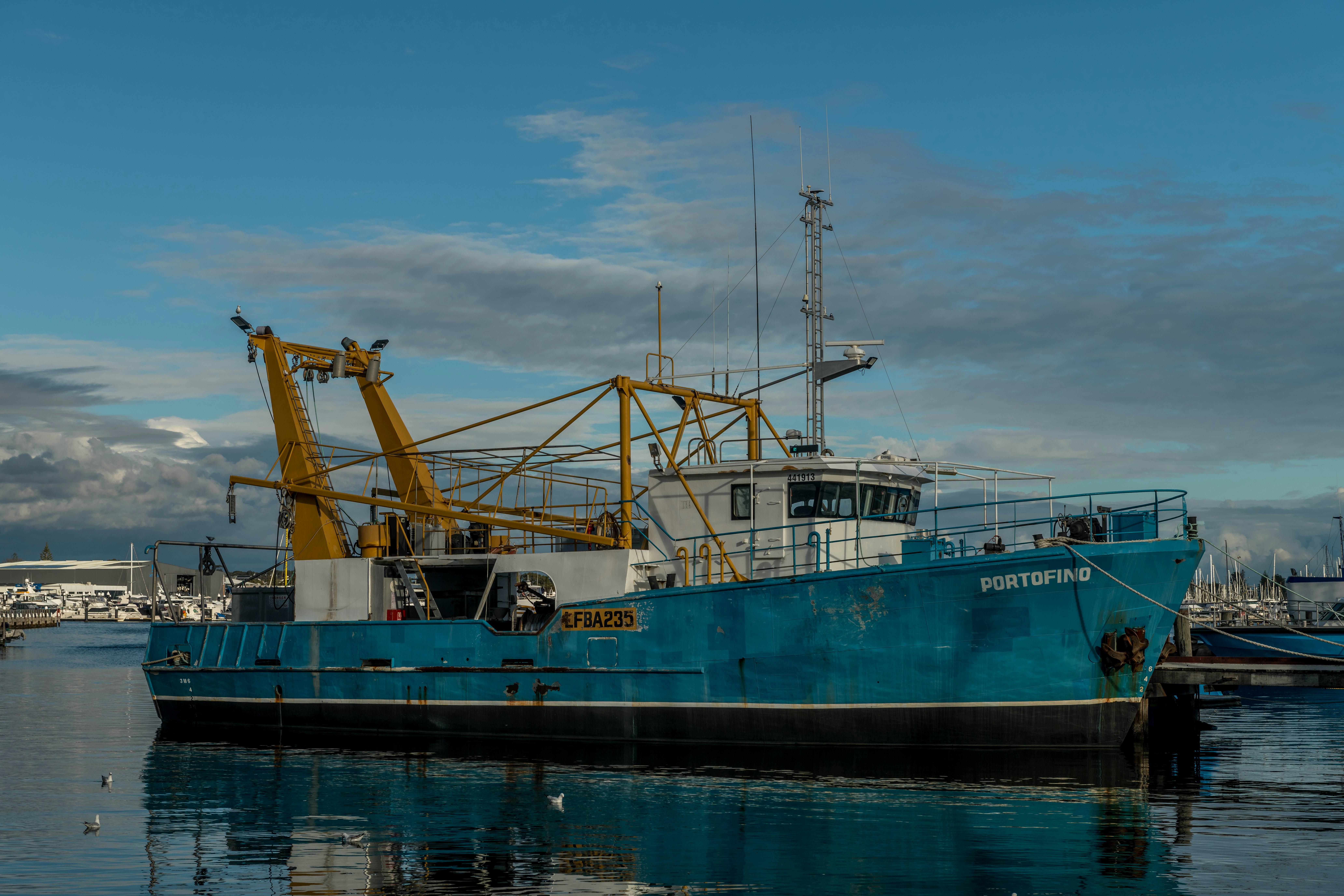 Fishing vessel 'PORTOFINO' rests peacefully in the harbor, reflecting the calm waters and blue sky above.