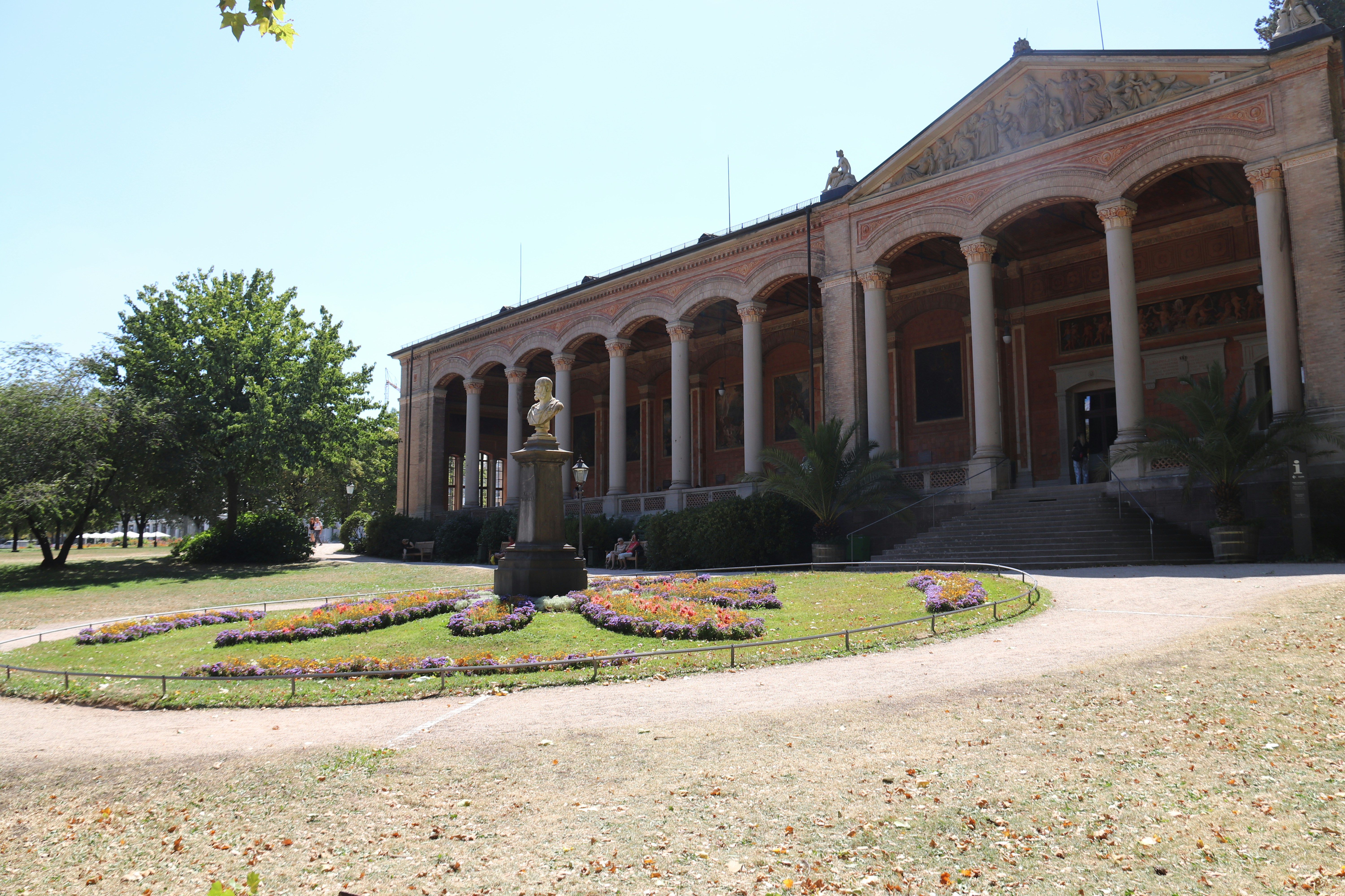 Historic building with grand columns and a manicured garden under a clear sky.