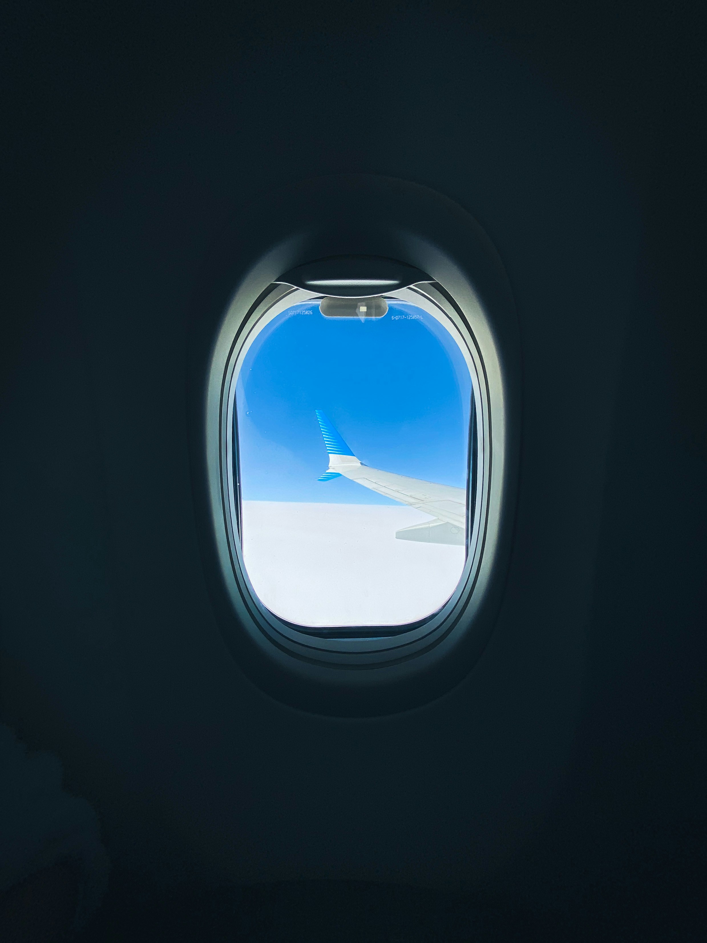 View through an airplane window revealing a wing against a backdrop of clear blue sky and soft clouds.