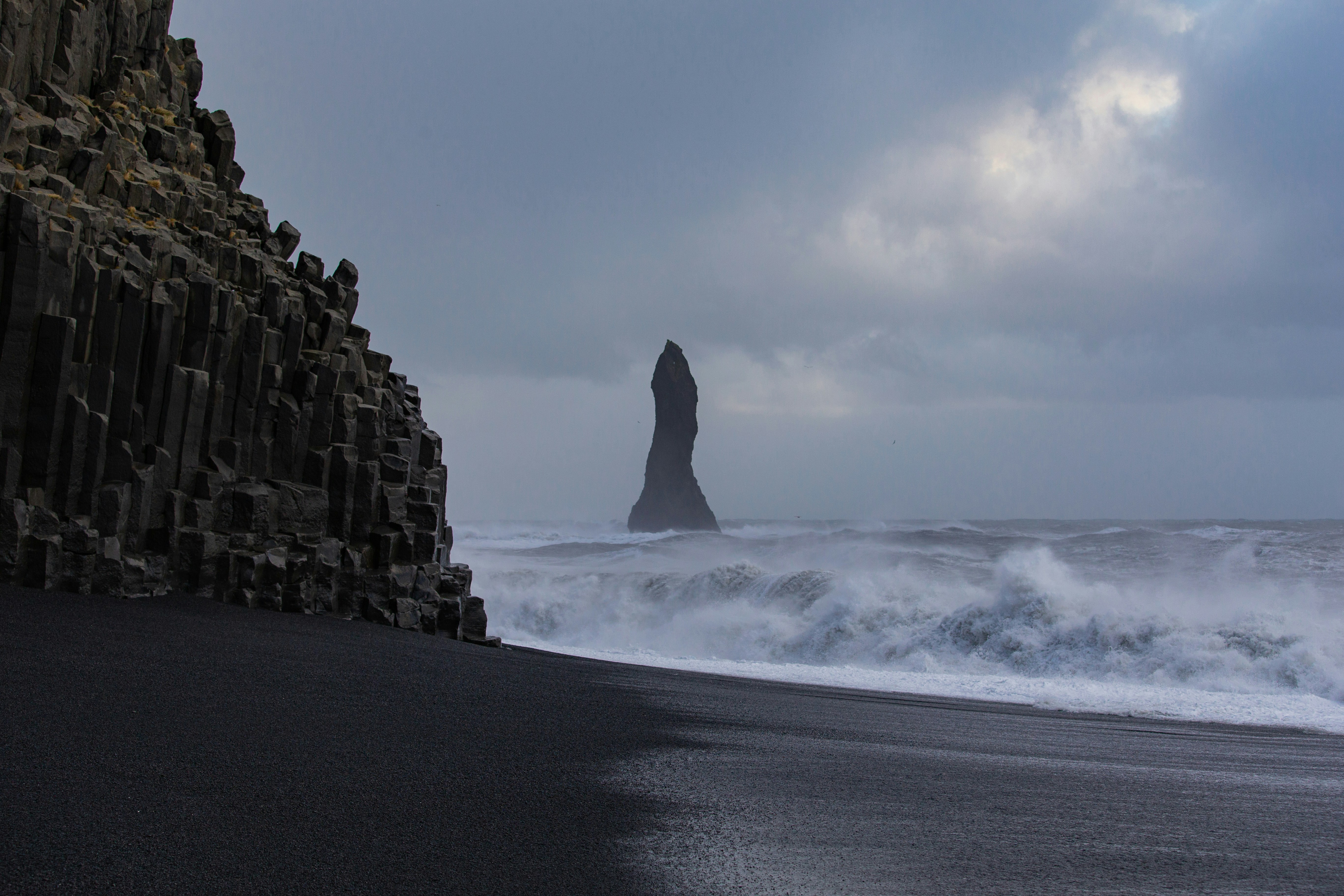 Sea Stack Rising Beyond Basalt Columns on a Dark Sand Beach