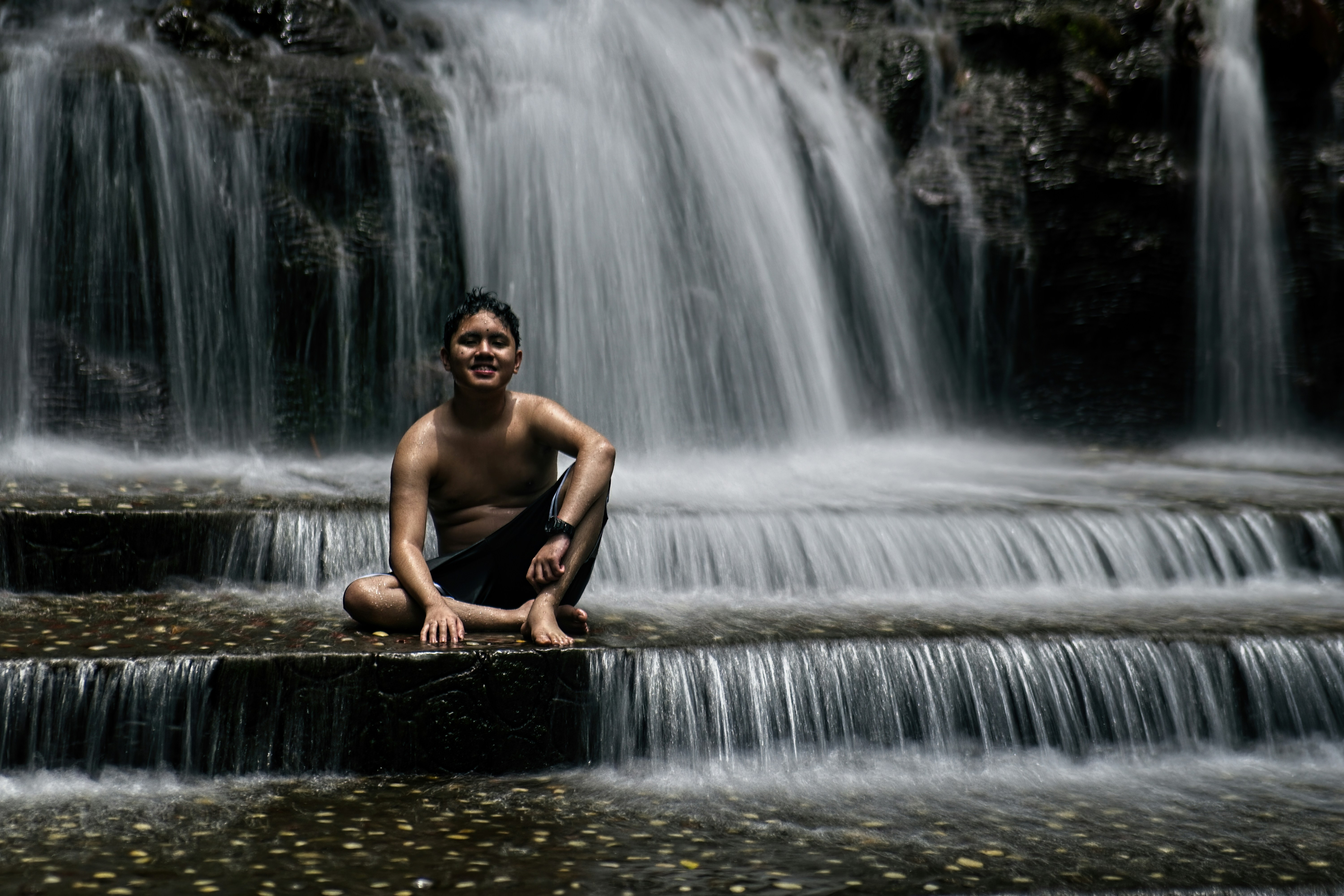 Person sitting on stone steps amid gently flowing waterfall.