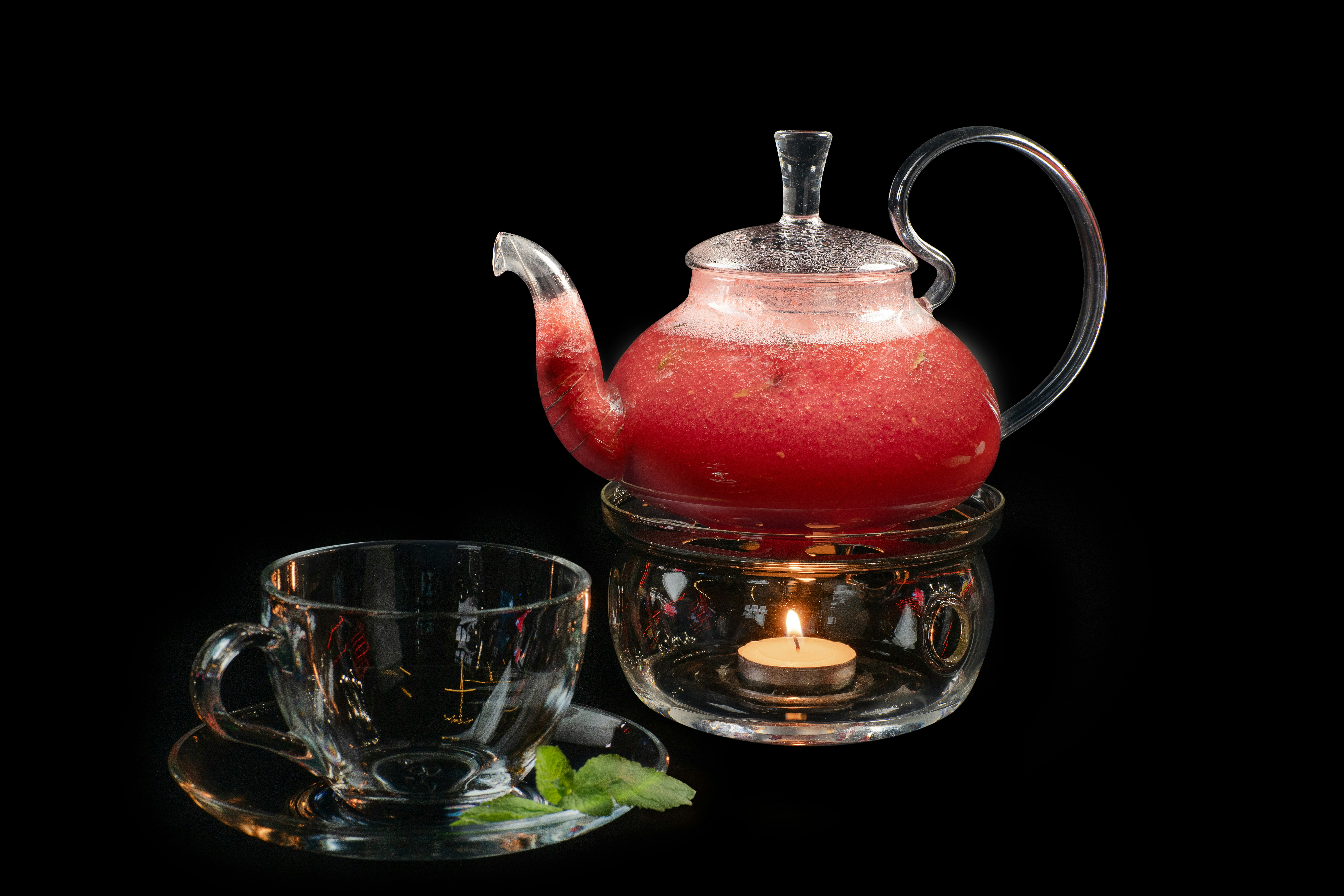 Crimson Infusion Aglow: Teapot Crowned by a Candlelit Glass Warmer