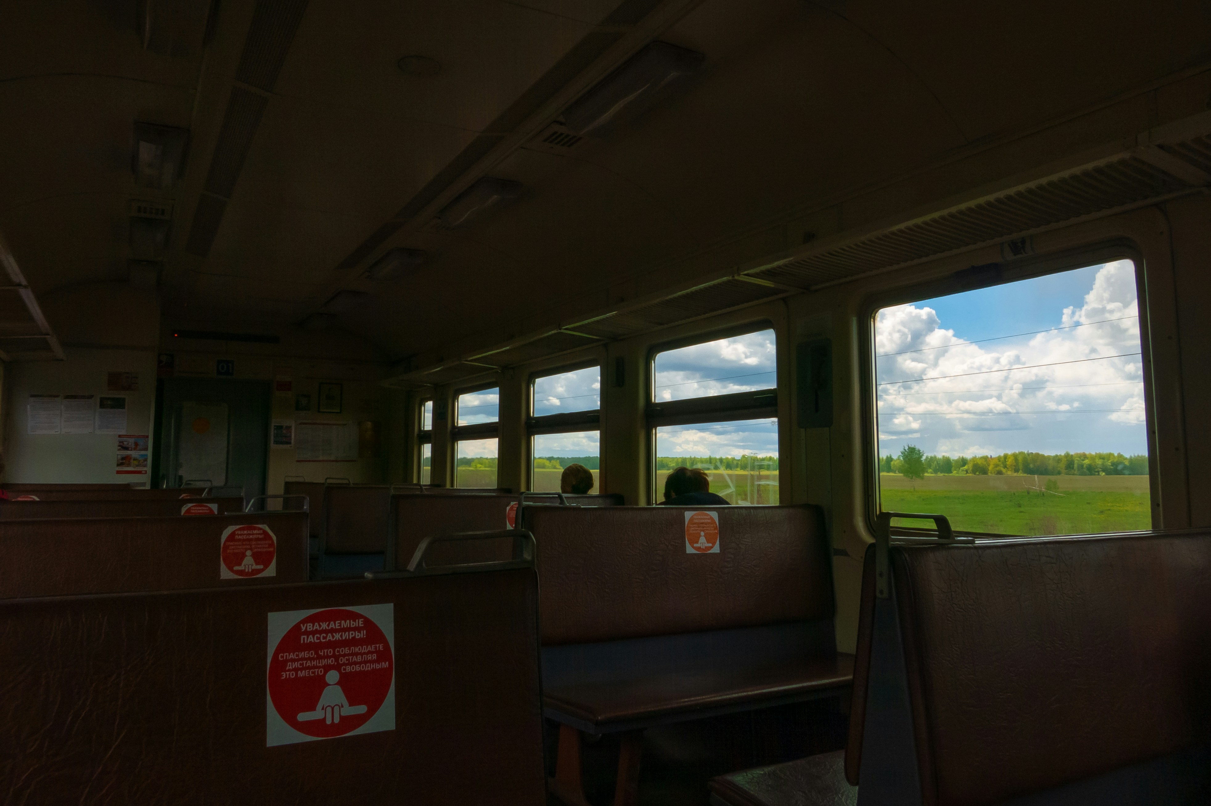 Empty train carriage with windows framing green fields and blue sky.