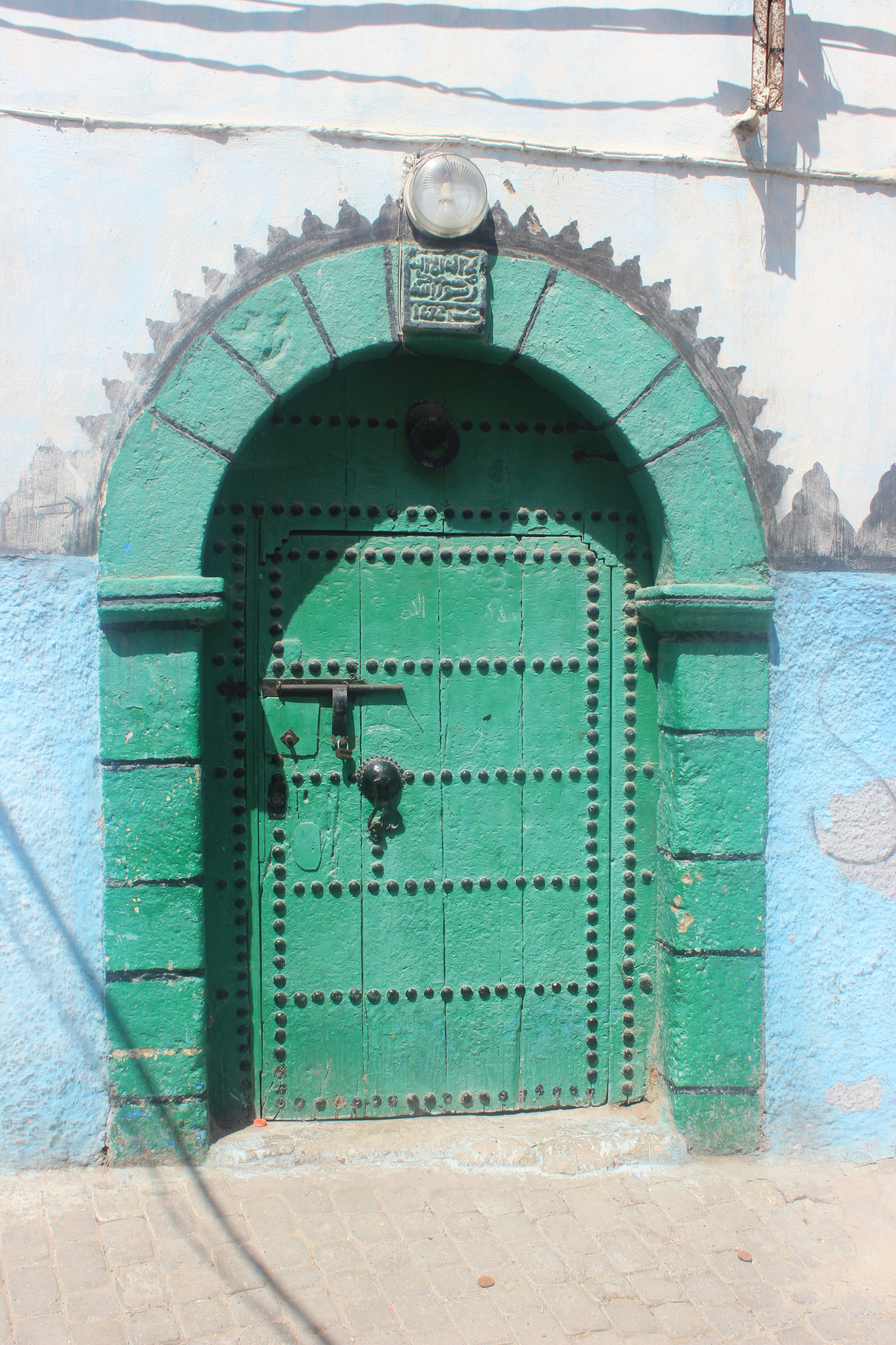 Riveted Green Door Under a Turquoise Arch on a Weathered Blue Wall