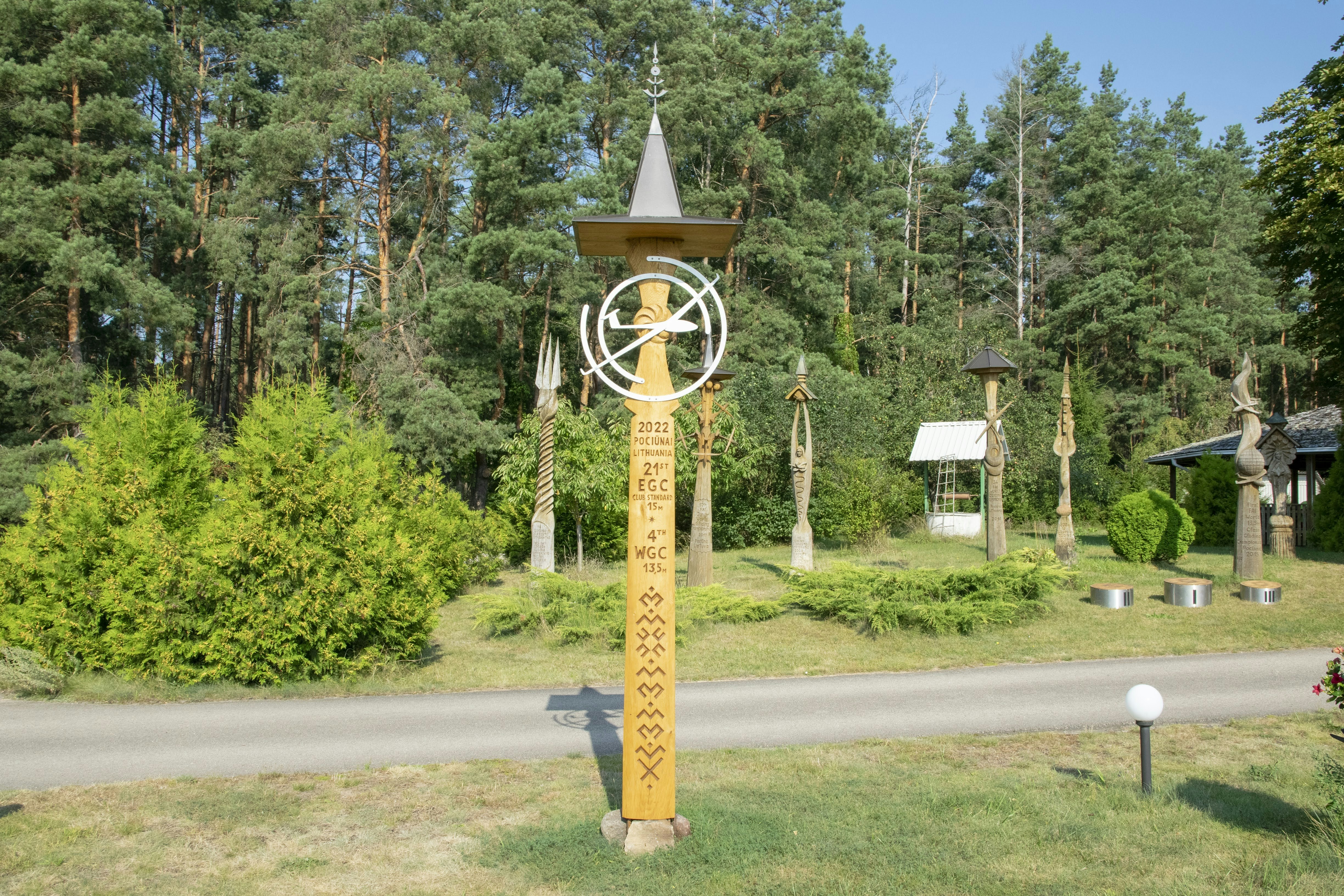 Compass-topped wooden pillar marks a sunlit forest road