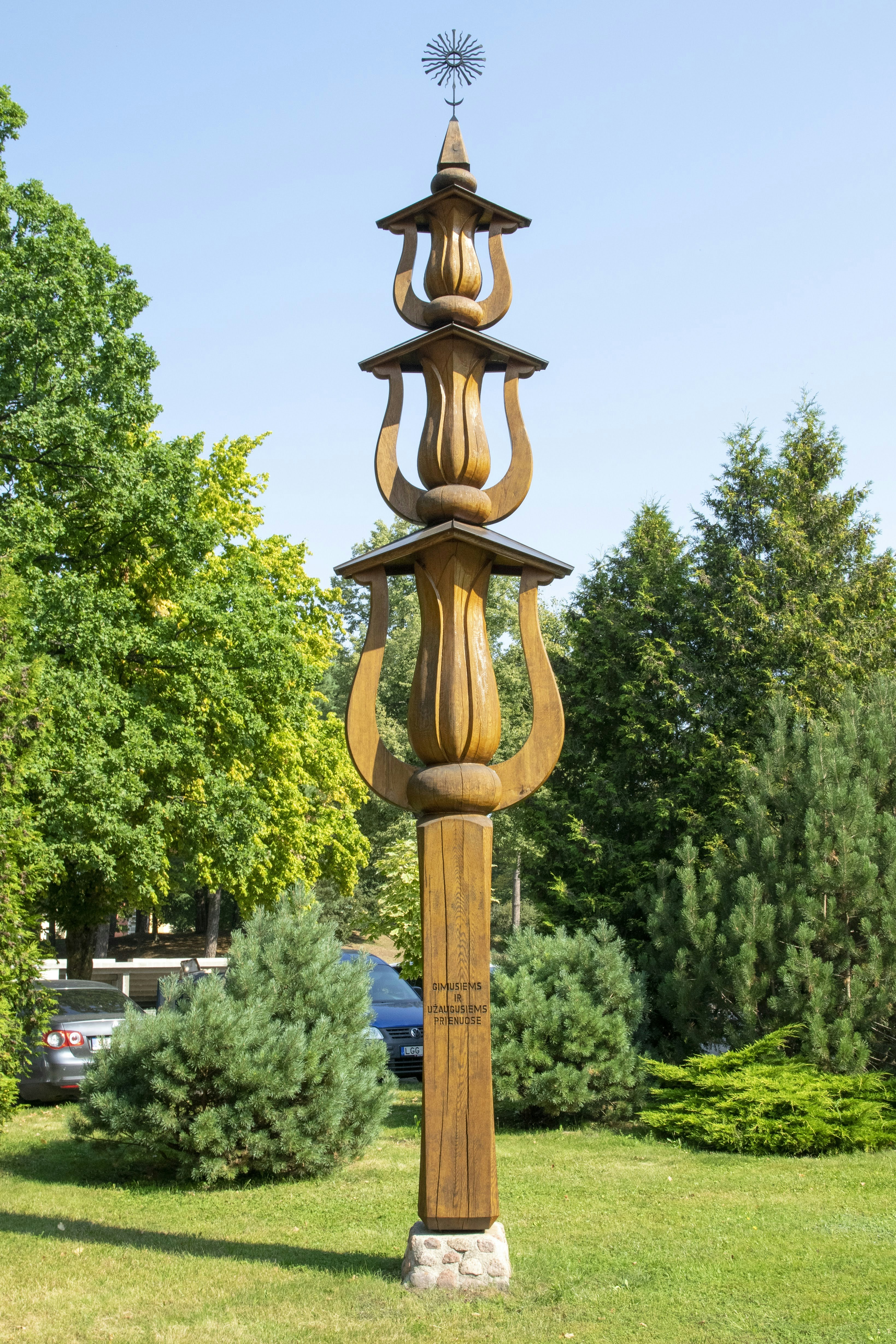 Intricately carved wooden spire showcasing traditional craftsmanship, surrounded by lush greenery. The structure features multiple tiers and a decorative finial.