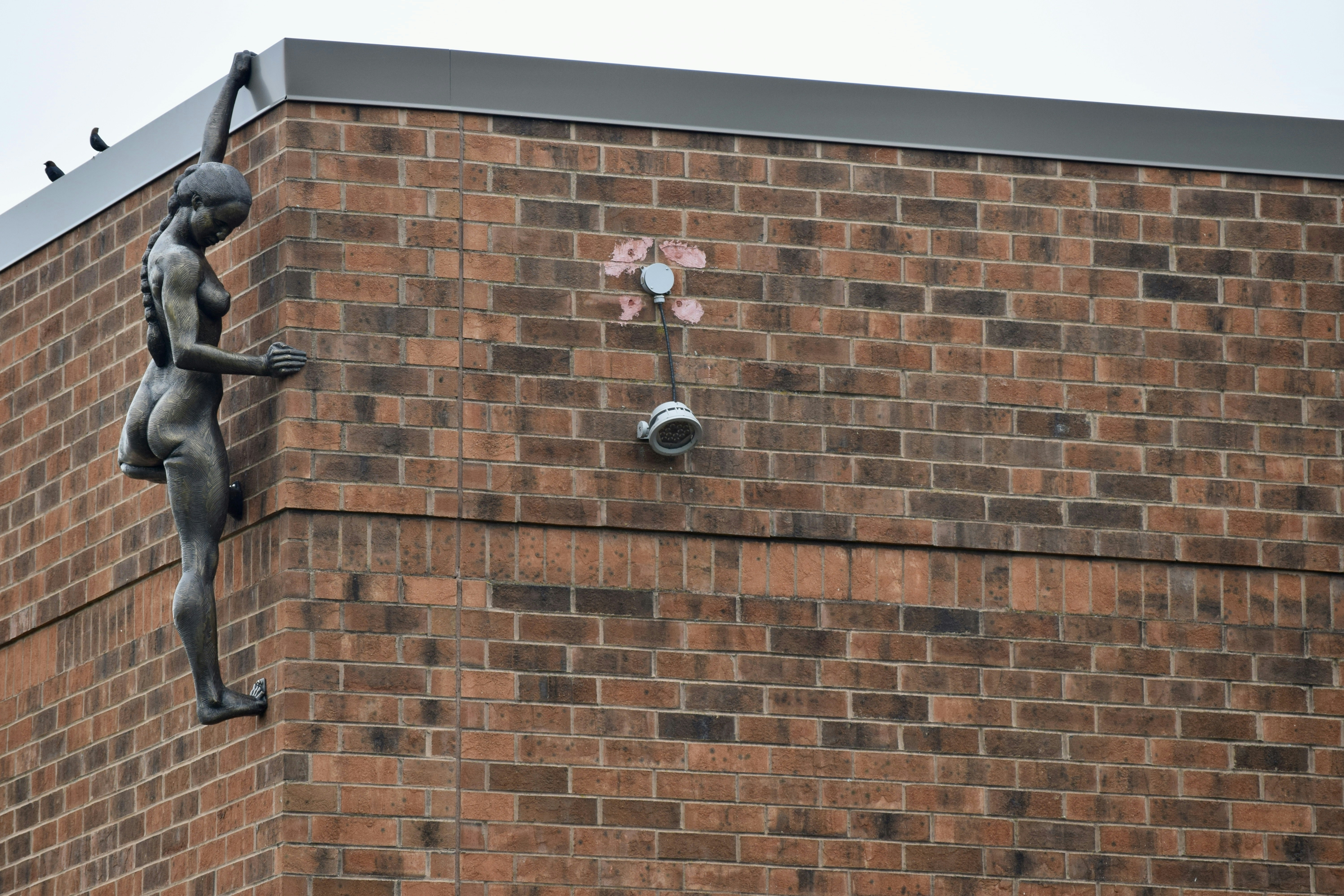 Climber on the Brick Corner: Bronze Figure Rises Along the Building Edge