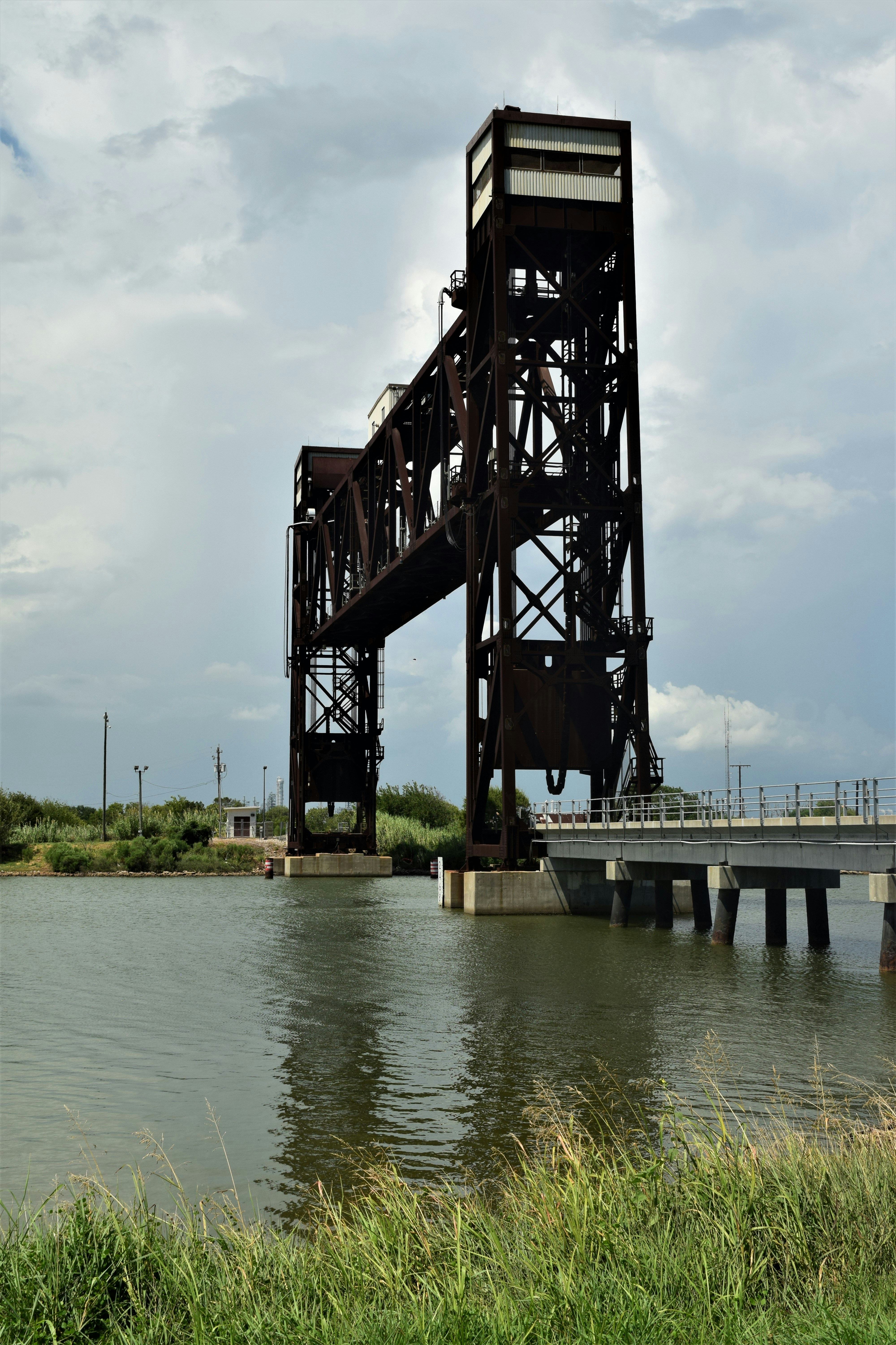 Iron Sentinel Over Quiet Water: A Rusted Lift Bridge Reaches Toward a Cloudy Sky