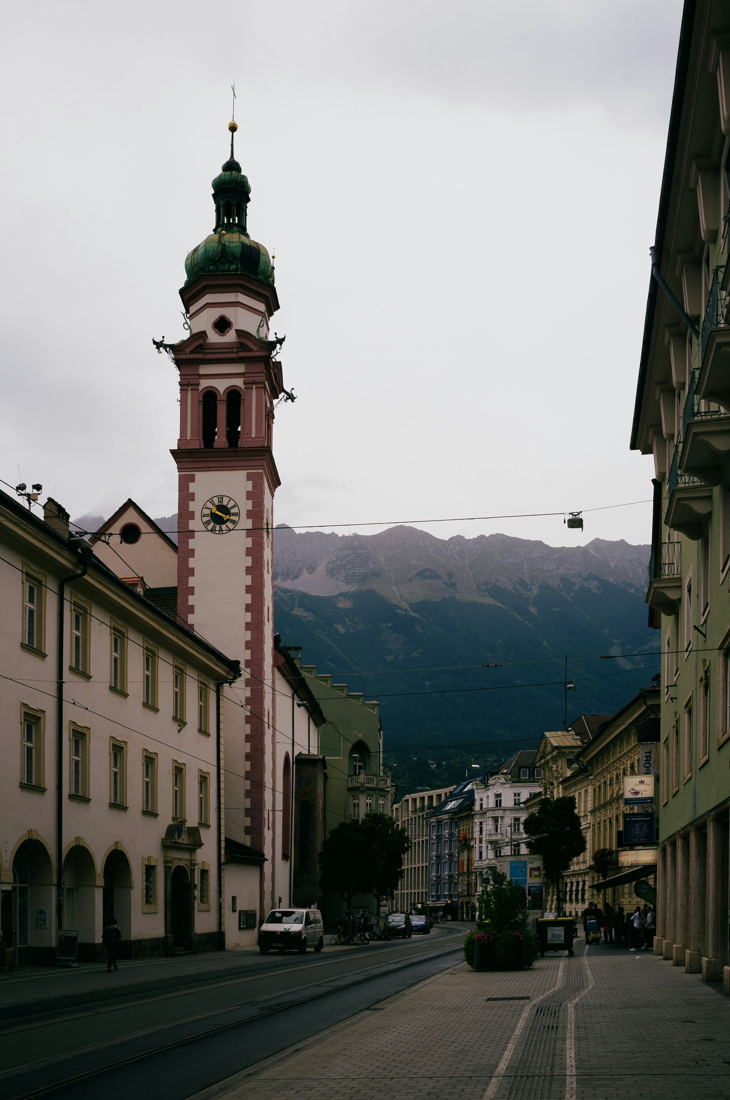 Historic clocktower stands tall amidst quaint buildings, with majestic mountains in the background. The scene captures a serene urban atmosphere.