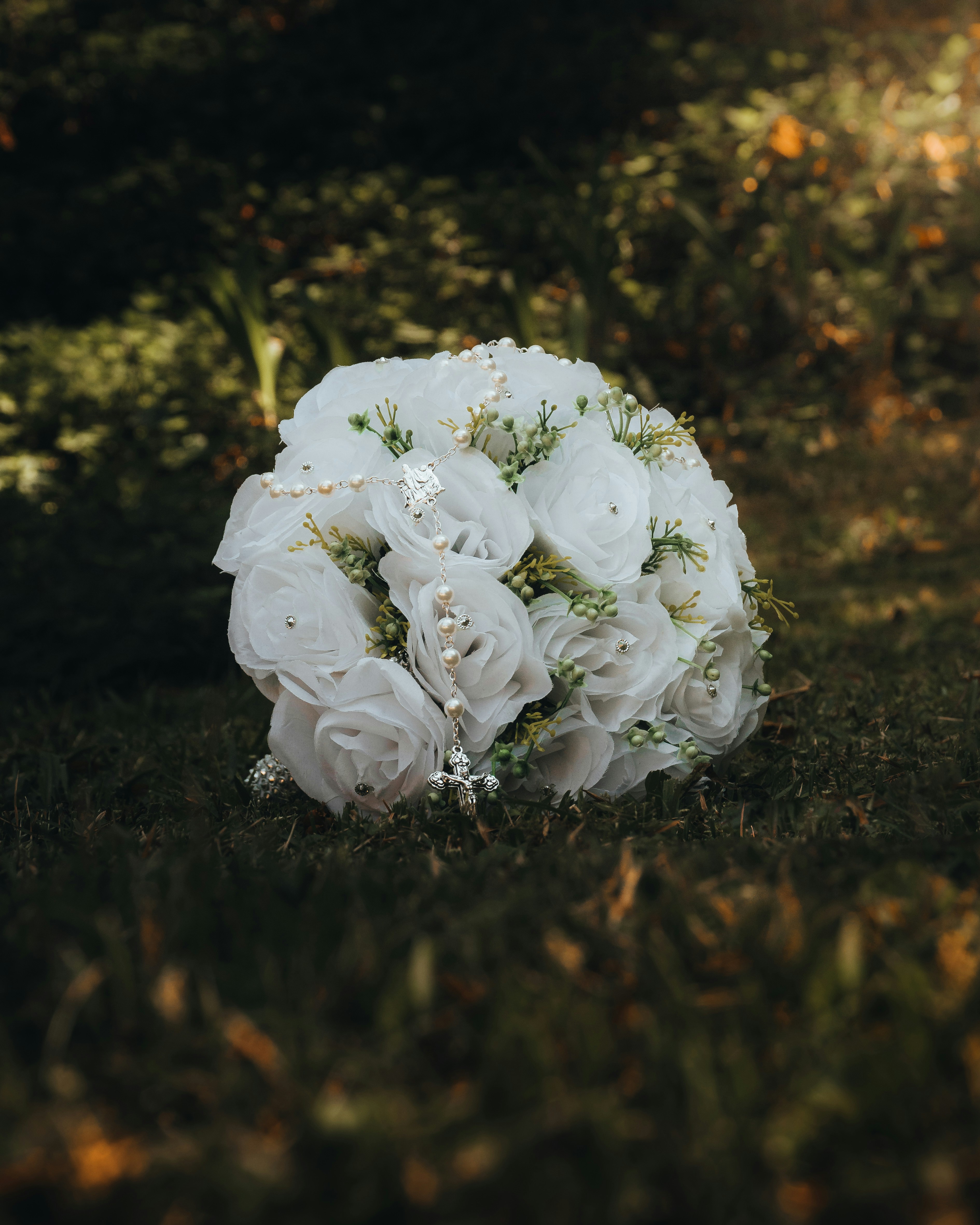 A beautifully arranged bouquet of white roses adorned with delicate greenery and pearl accents resting on a grassy surface.
