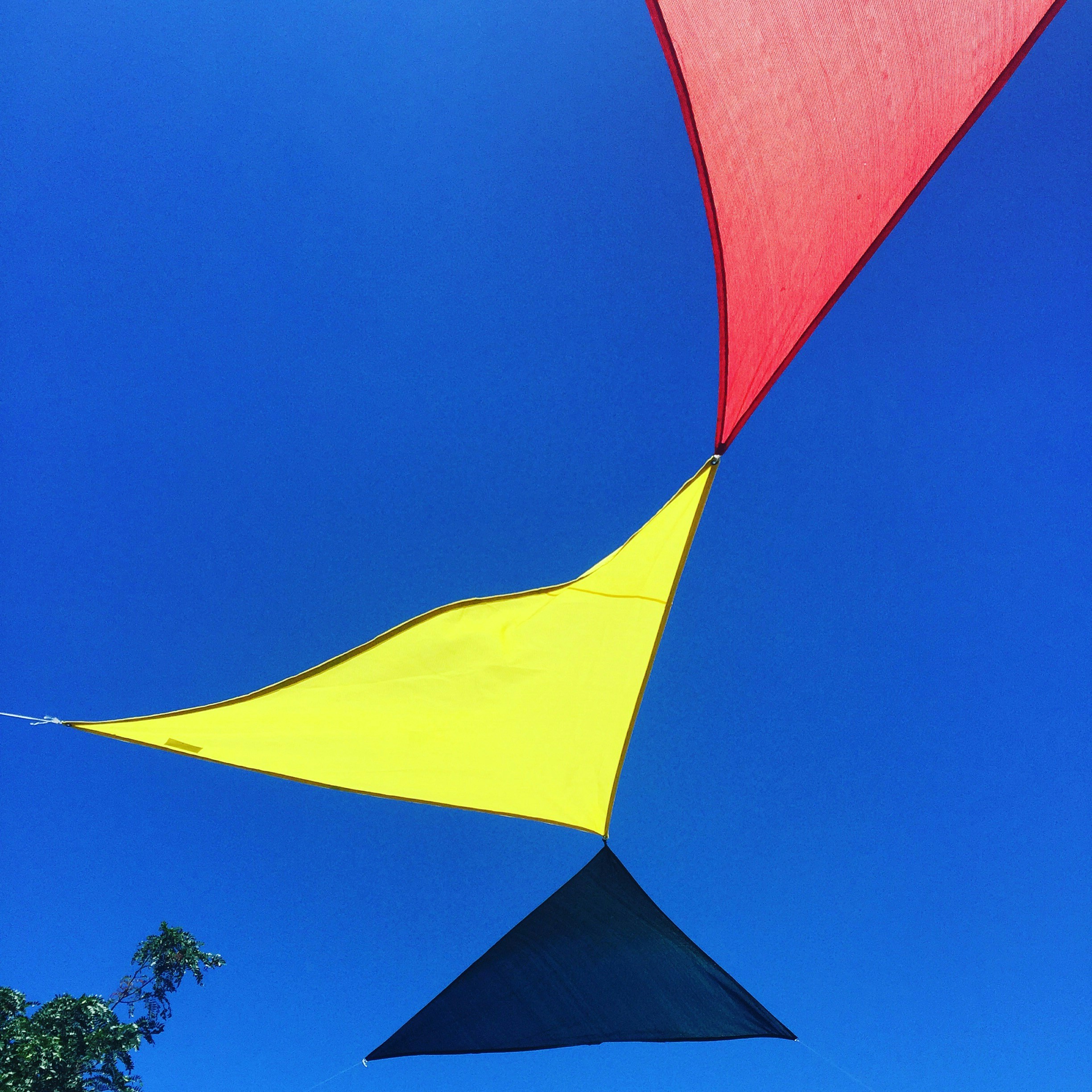Colorful triangular sails in red, yellow, and black contrasted against a bright blue sky.
